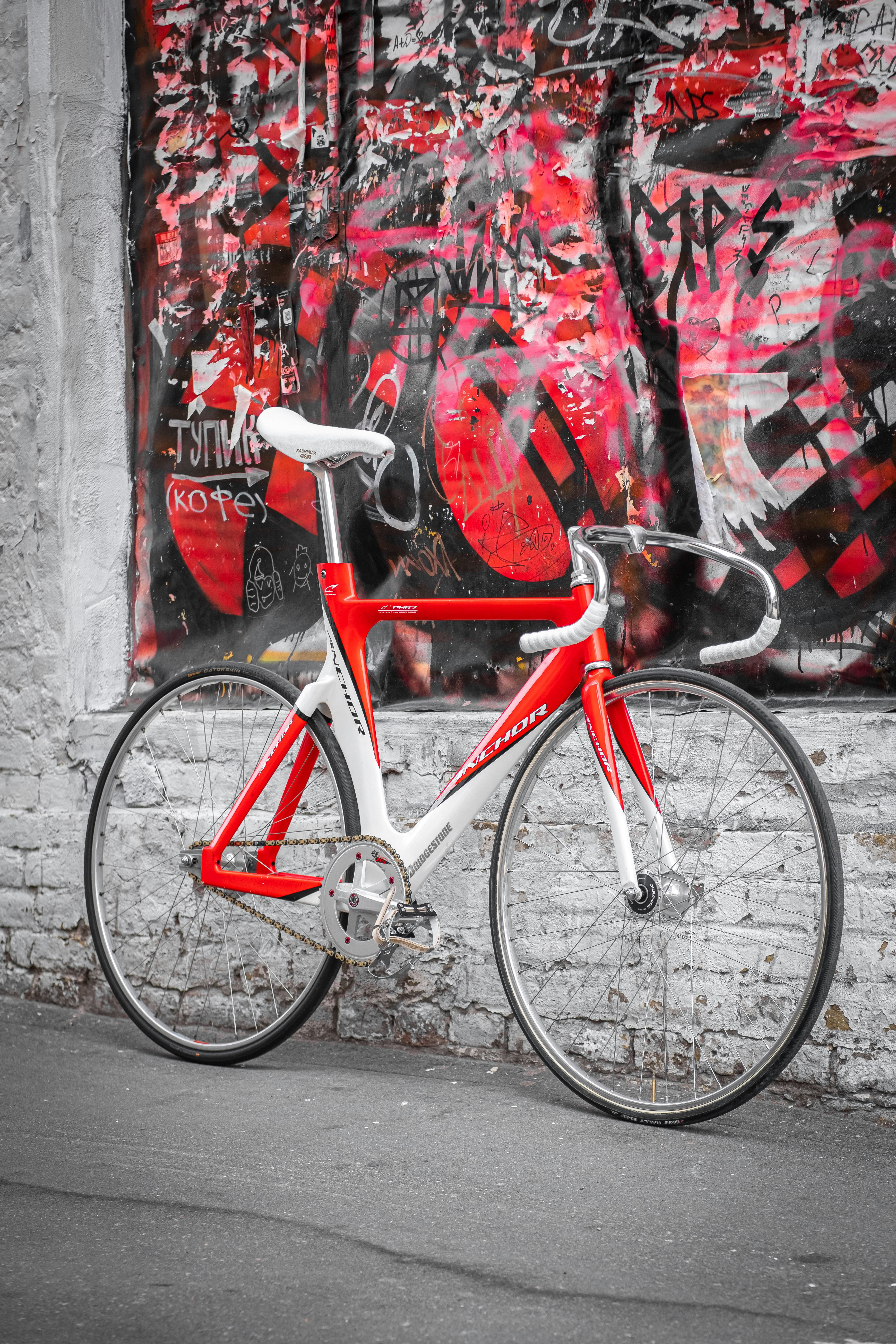 A sleek, modern bicycle stands against a vibrant graffiti wall, showcasing a striking contrast between its red and white design and the chaotic background.