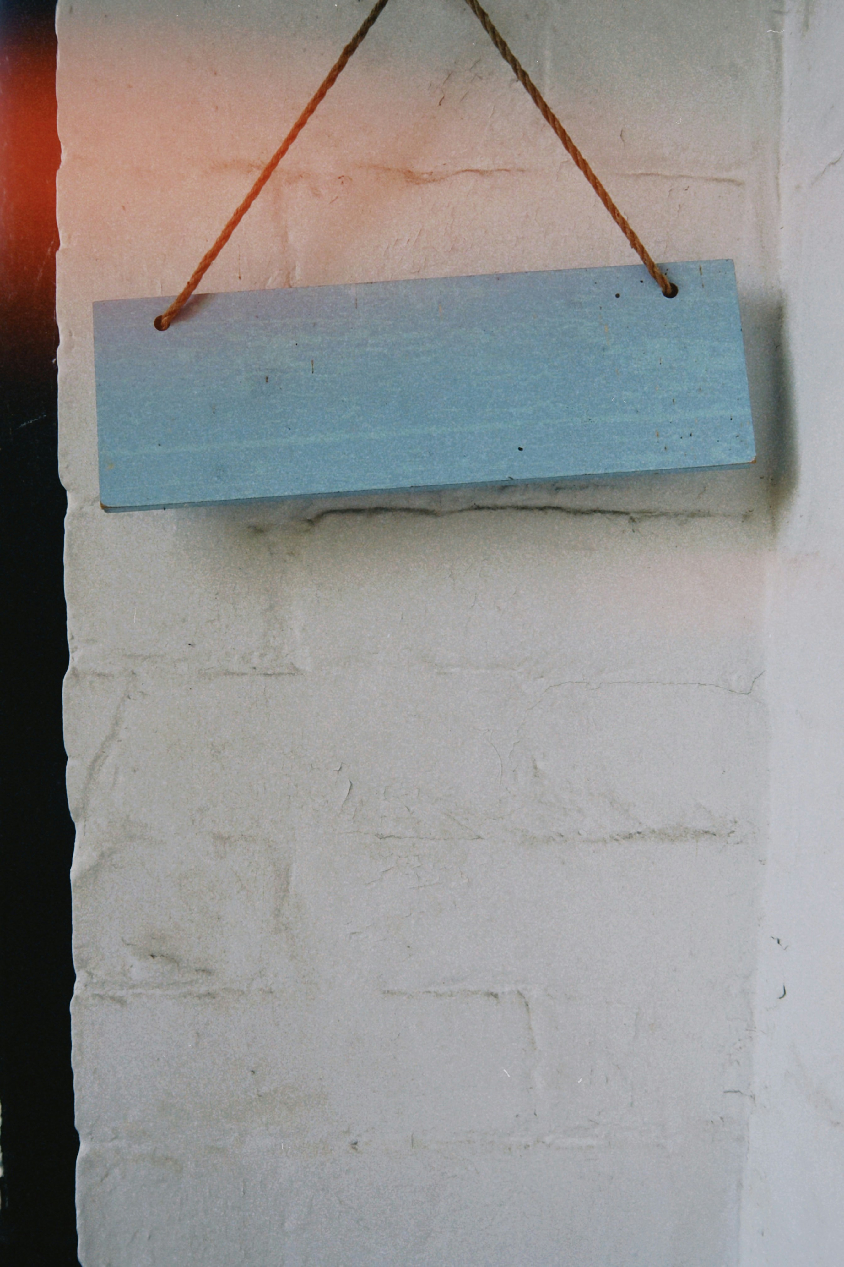 A blank blue sign hangs on a white wall.