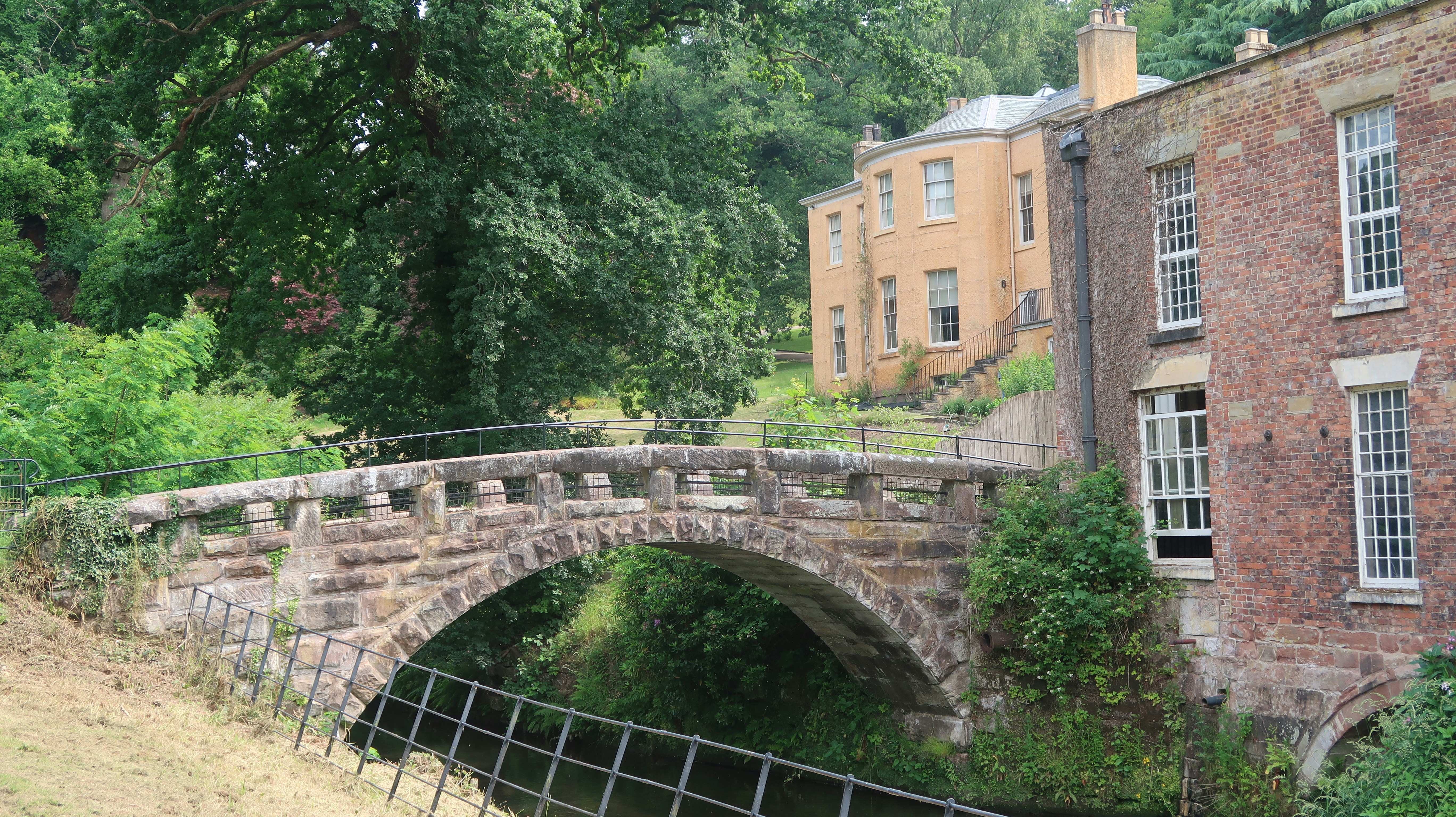 Stone bridge arching over a tranquil canal, flanked by lush greenery and historic buildings.