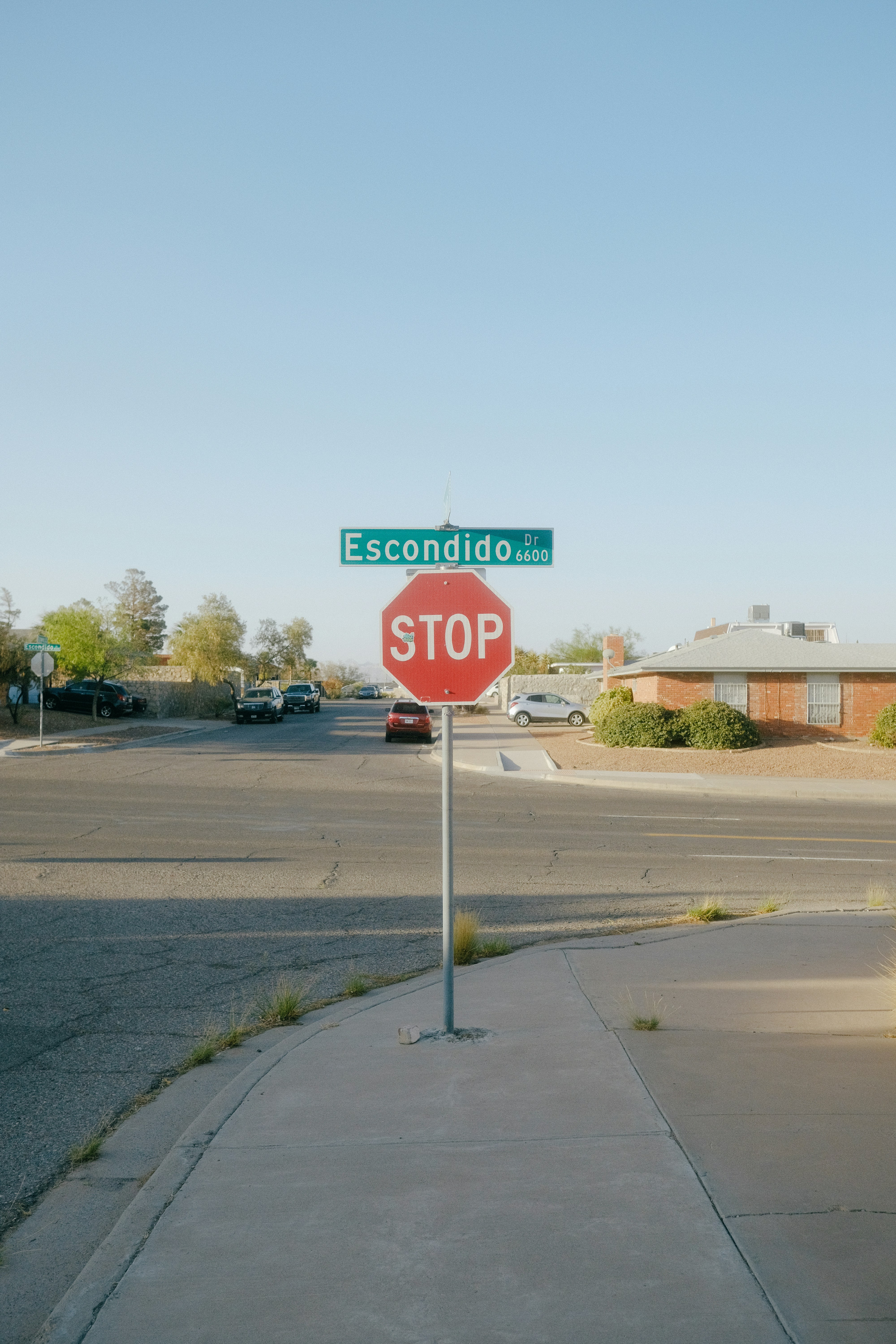 Stop sign at the intersection of Escondido Drive, with vehicles and buildings in the background. Clear blue sky enhances the scene.
