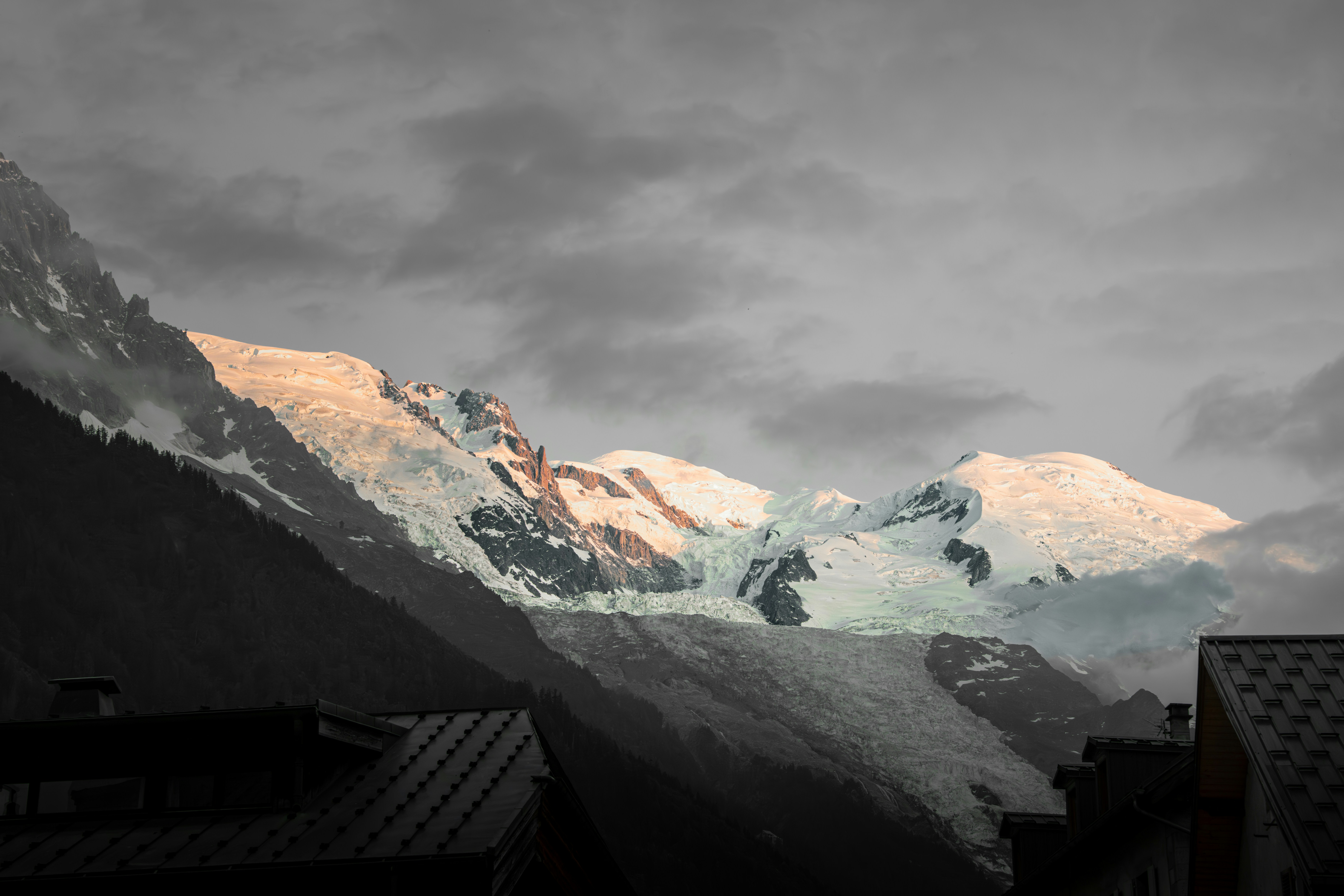 Snow-capped mountains glisten under the soft morning light, framed by dark, shadowy valleys and rooftops below.