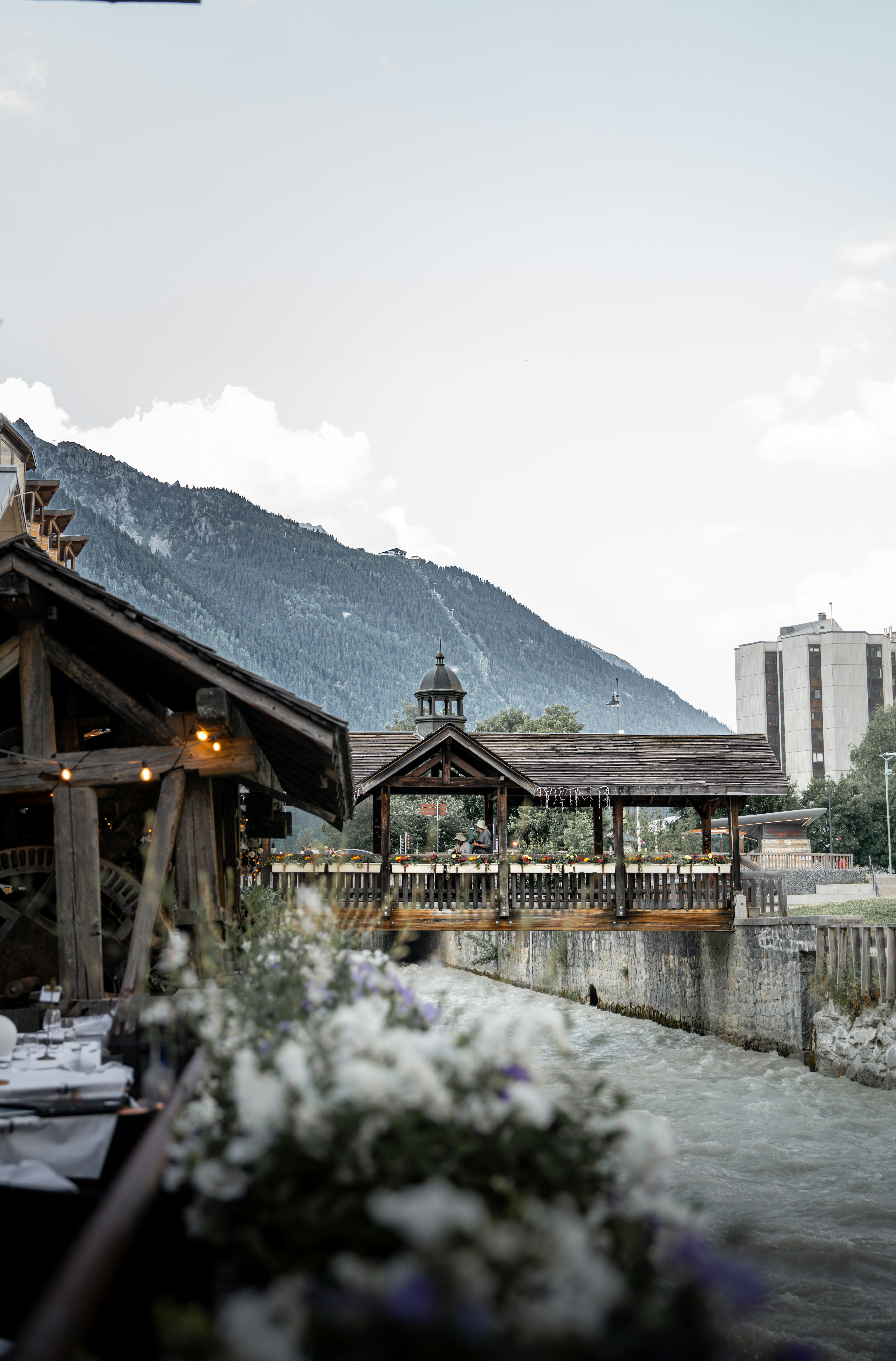 Wooden riverside pavilion extending over a rushing current under alpine backdrop