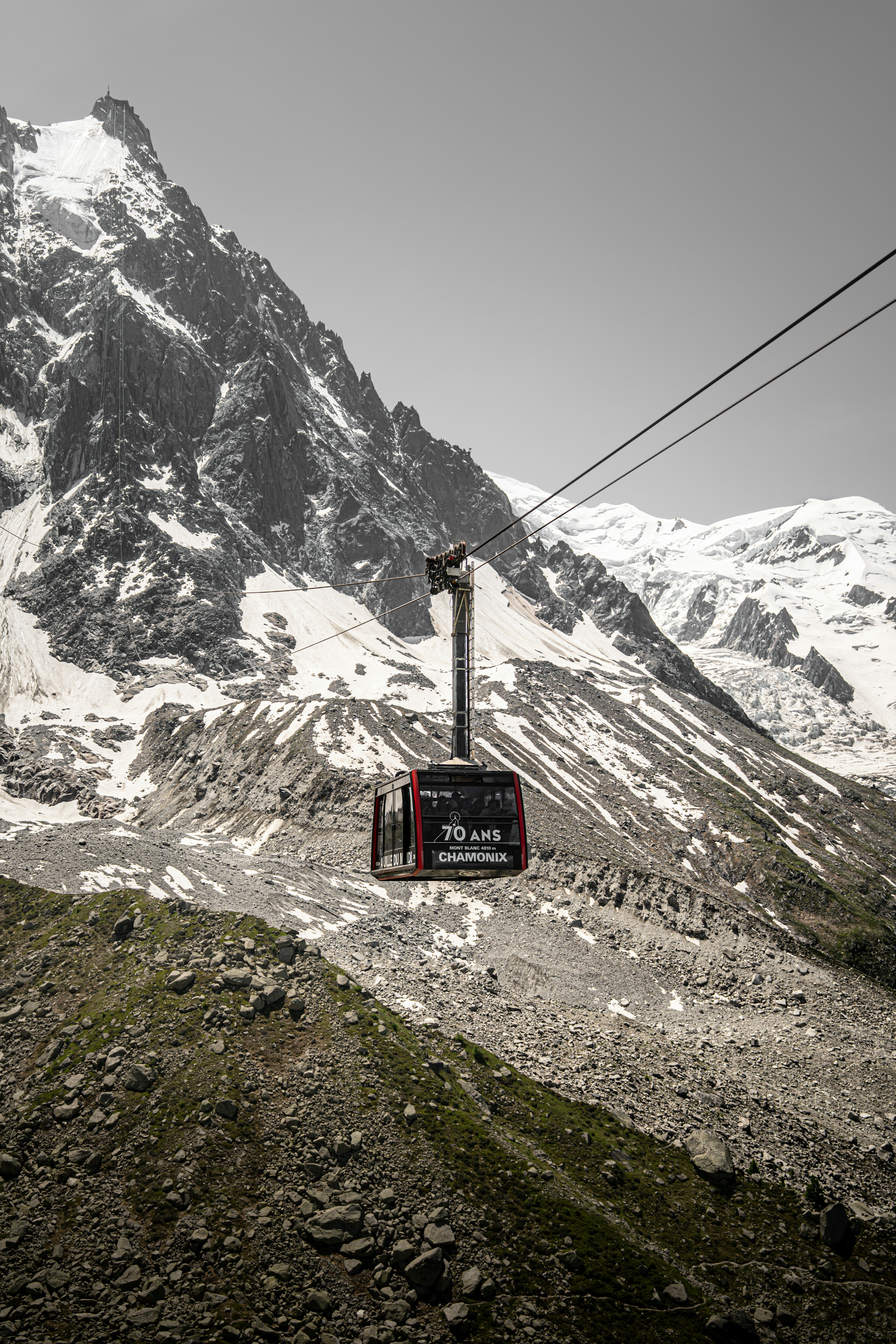 A gondola gliding over rugged terrain towards snow-capped peaks in Chamonix, showcasing the contrast between nature's raw beauty and human ingenuity.