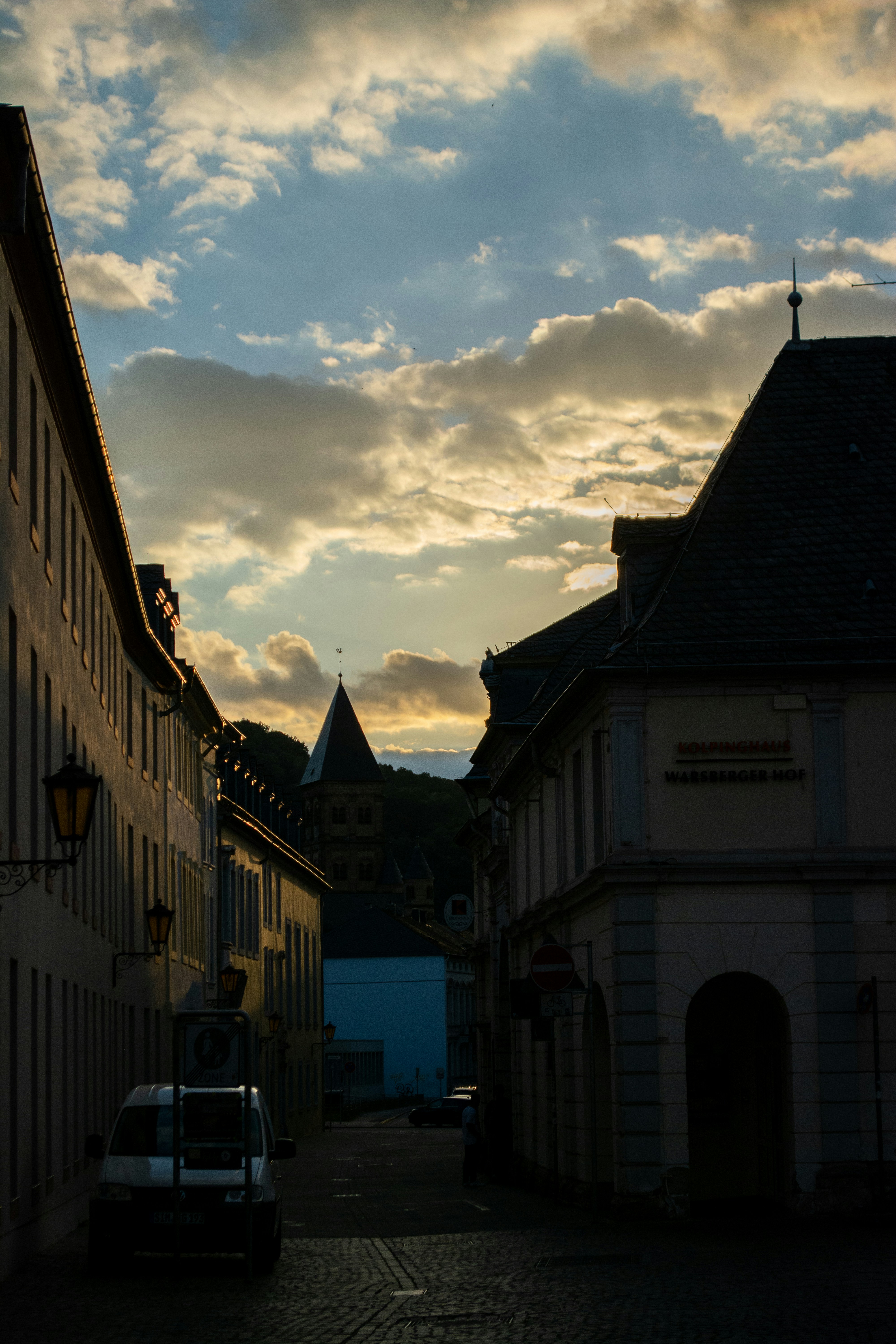 Silhouetted buildings line a cobblestone street under a dramatic sky, hinting at the history of the area. The scene captures the essence of a quiet evening as daylight fades.