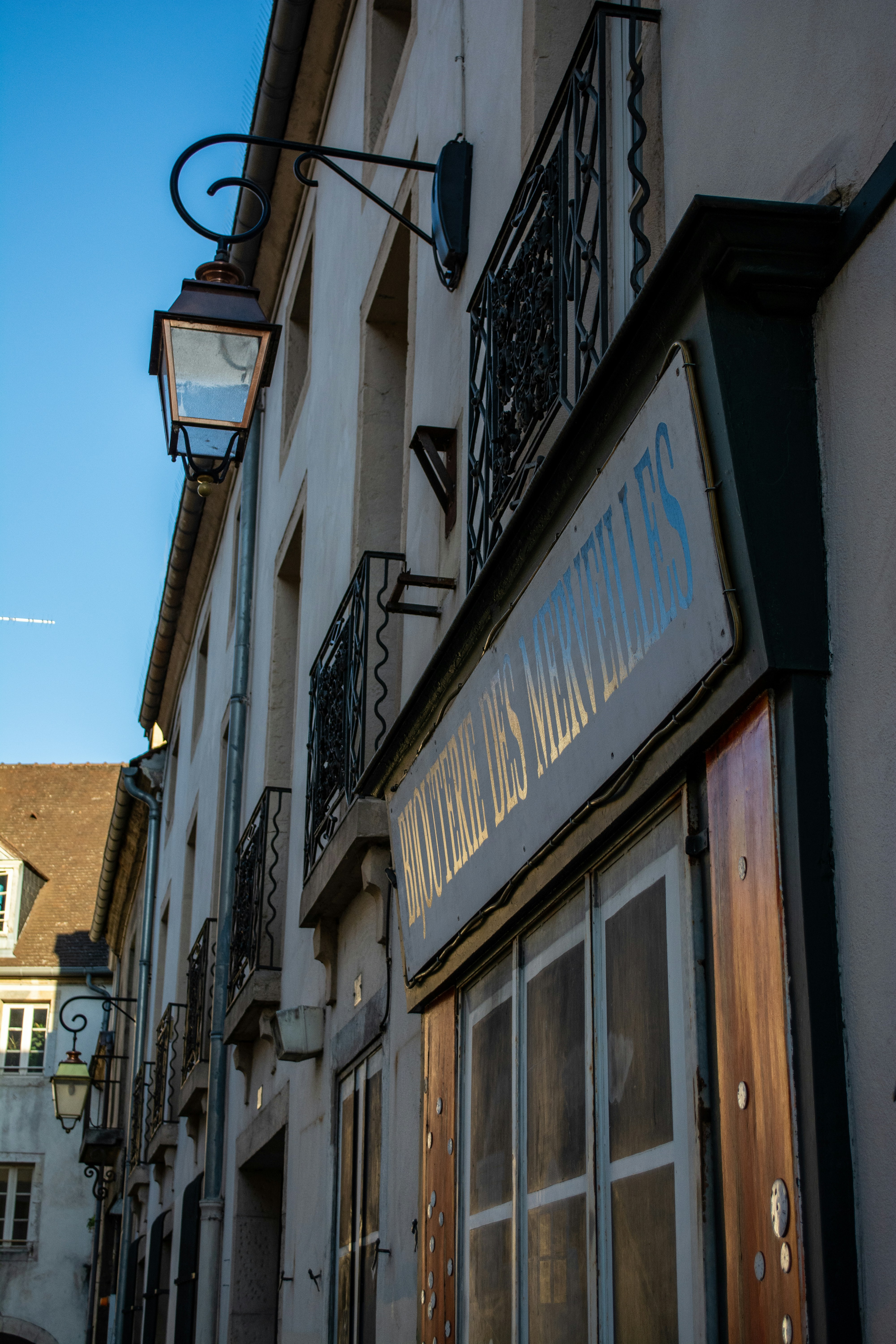 A narrow street in Dijon glows in the evening light, featuring a charming shopfront labeled "Bijouterie des Merveilles" beneath classic wrought-iron balconies and vintage lanterns. The warm reflections and architectural details evoke the timeless elegance of old French towns. | Old european buildings with ornate details.