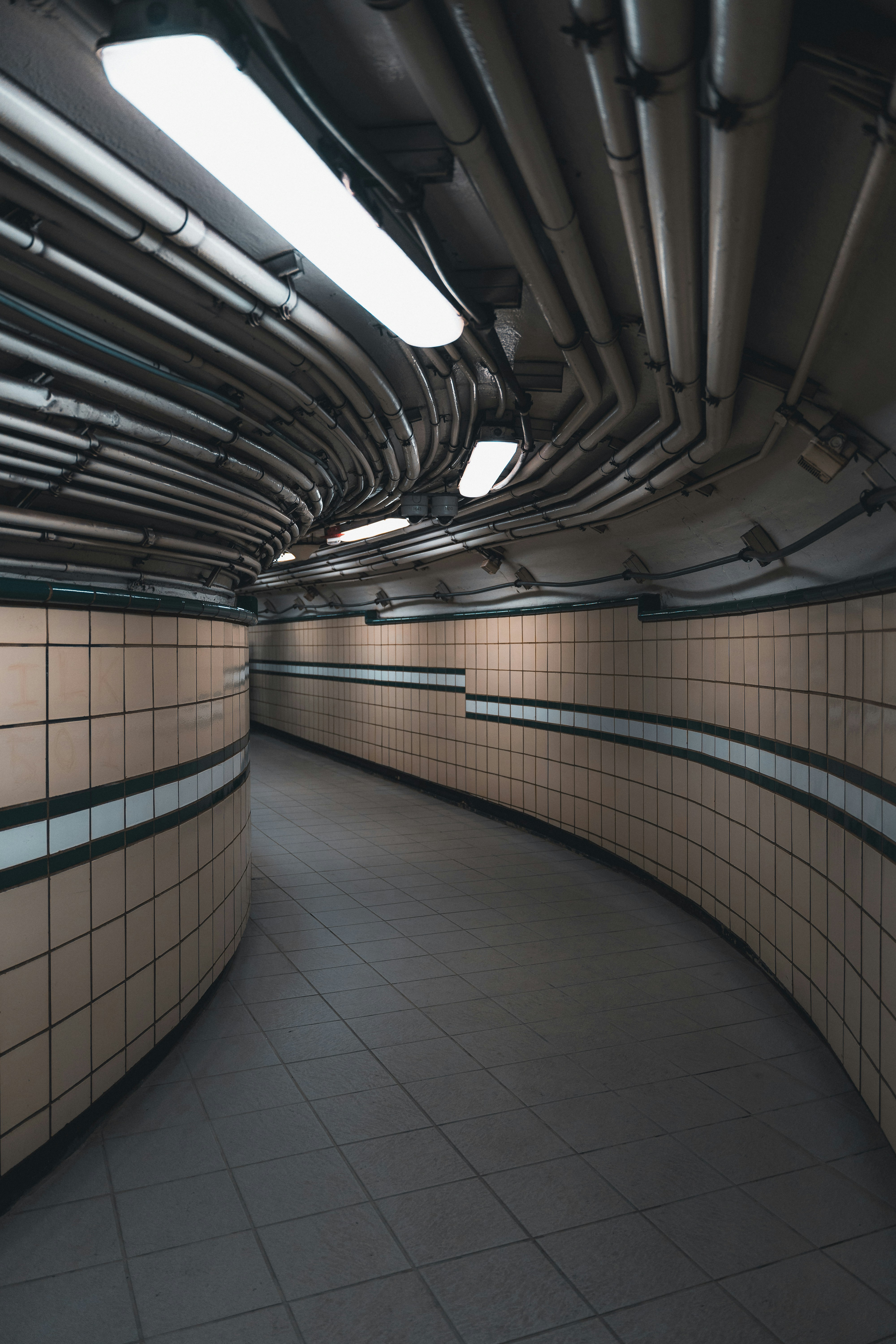 A curved, tiled hallway with overhead pipes. photo – Free Train Image ...