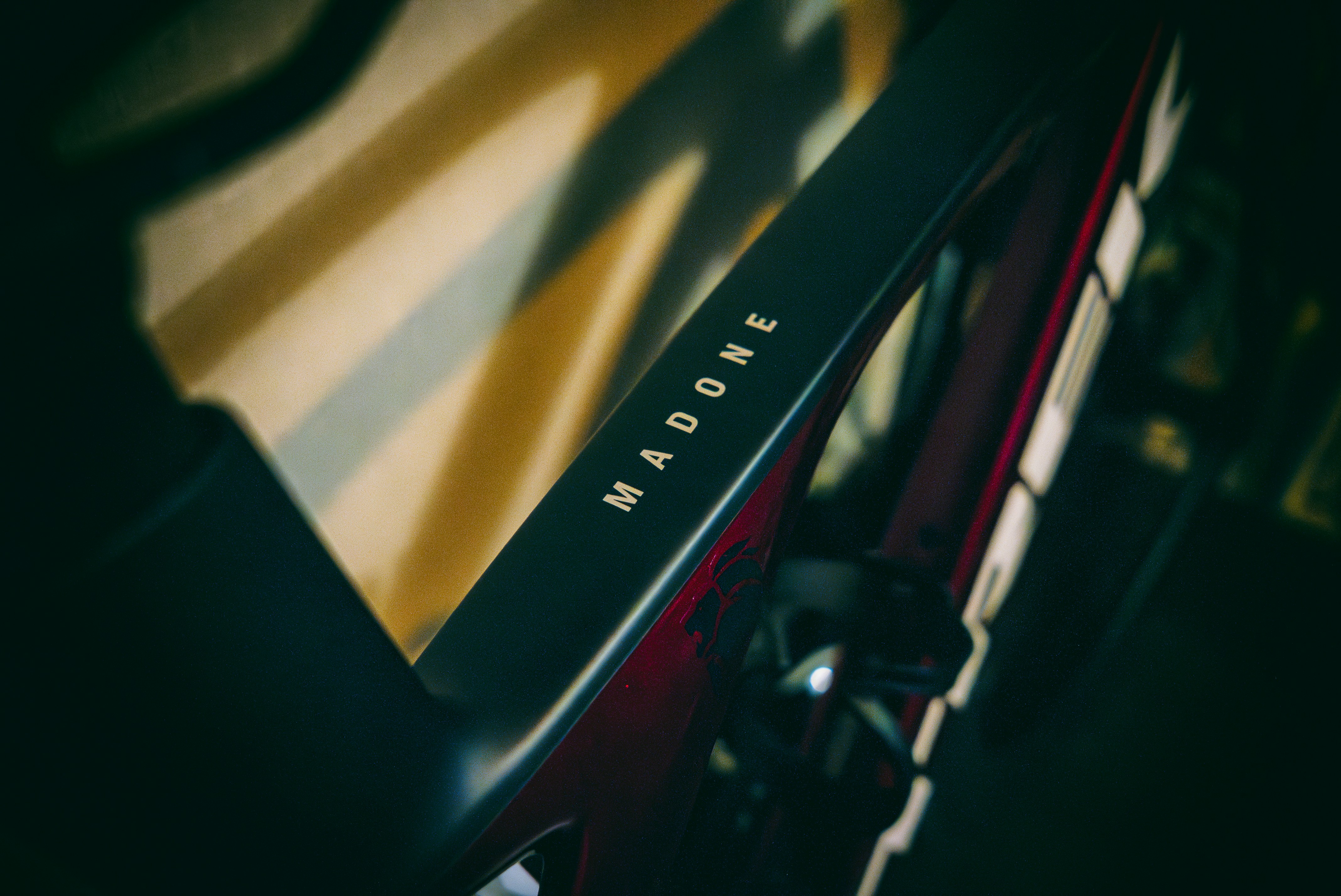 Close-up view of a bicycle frame showcasing the brand 'MADONE' in a stylish font against a blurred background.