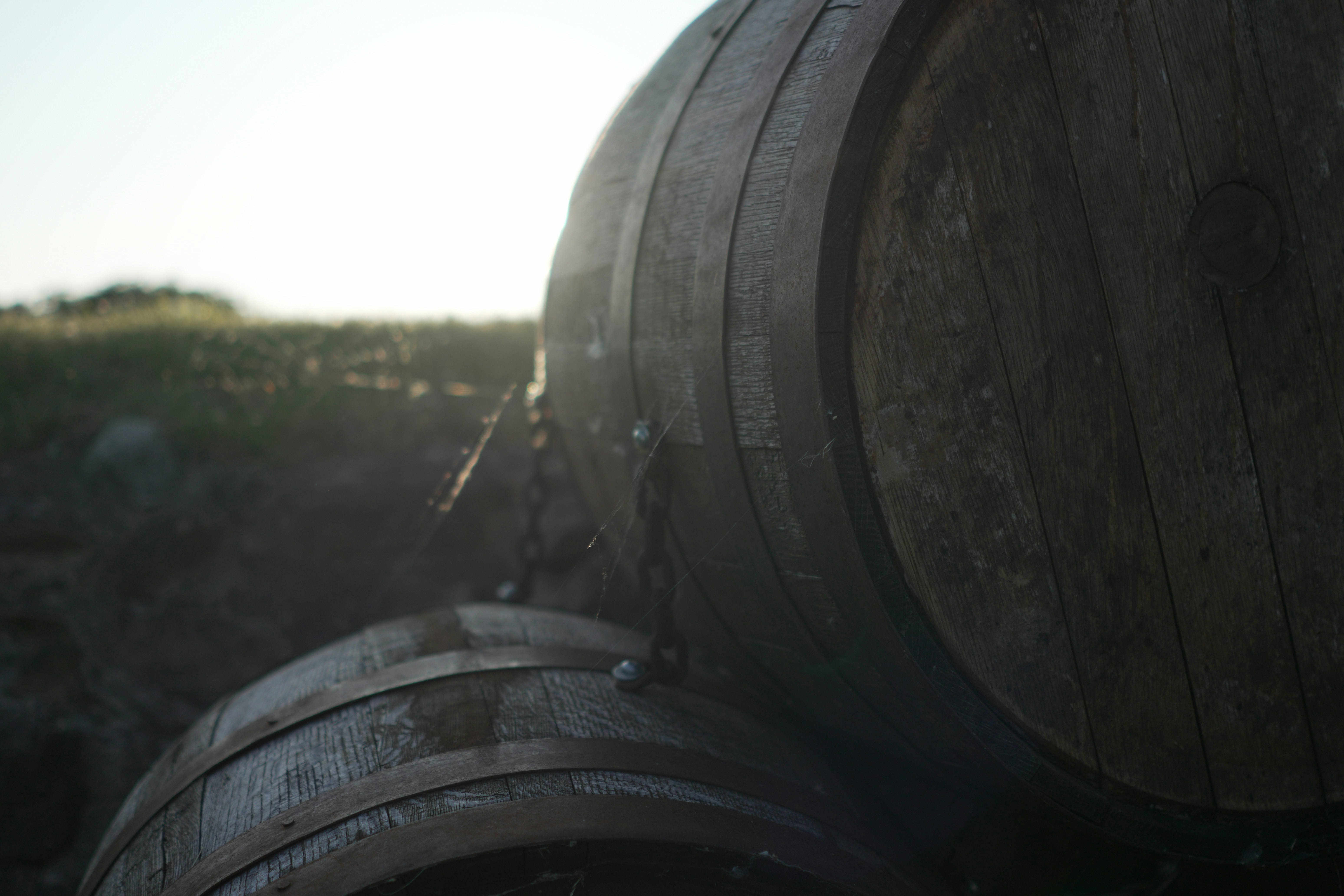 Wooden barrels are stacked outdoors in the sunlight.