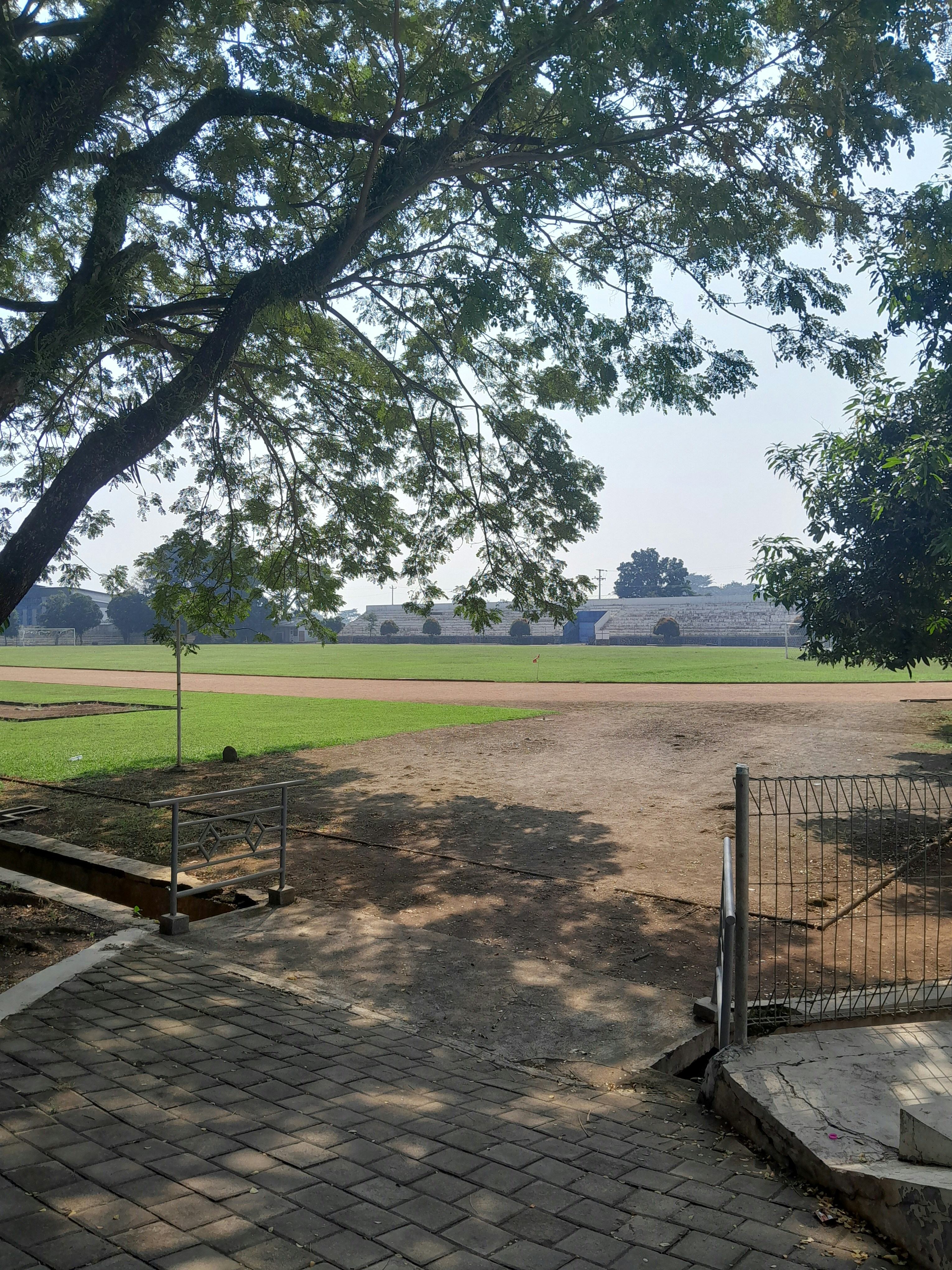 A serene pathway leading through a lush green field, framed by trees and distant structures, inviting exploration.