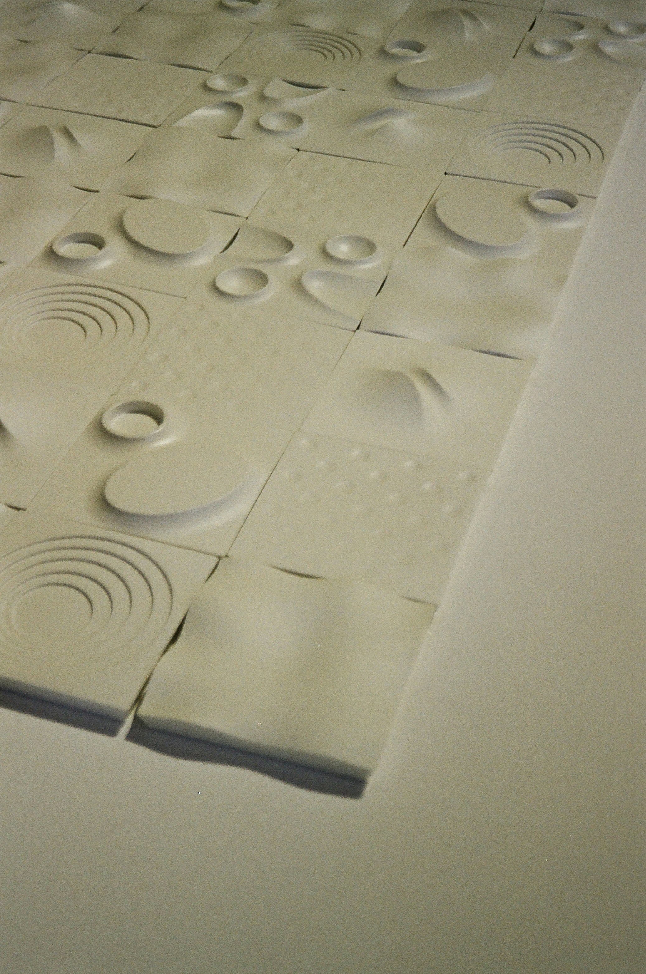 Close-up of embossed, tiled pattern with circular and curved shapes casting gentle shadows; a minimalist, textured surface likely in a showroom or product display.
