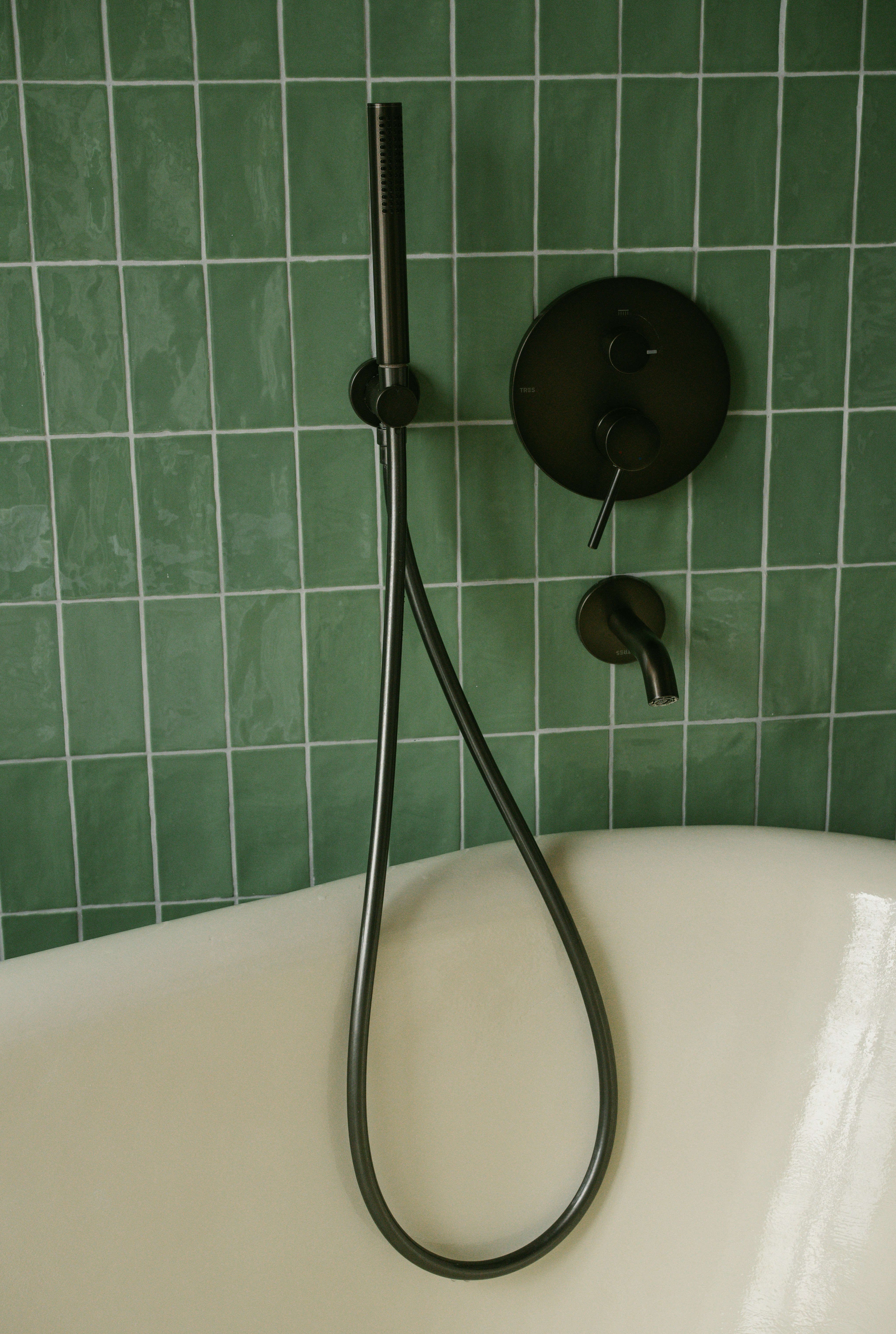 Sleek black showerhead and faucet against a textured green tiled wall, highlighting contemporary bathroom design elements.