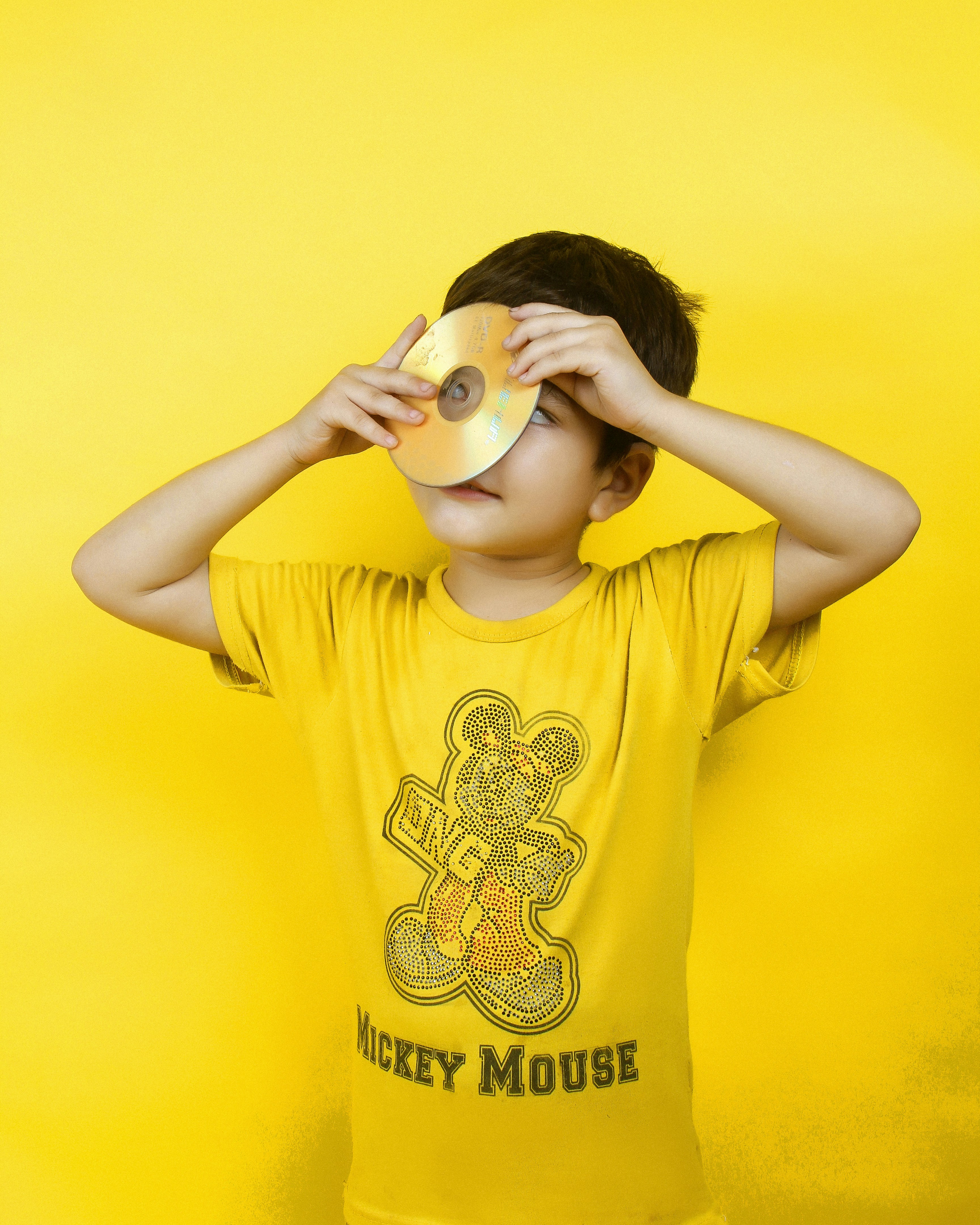 CD Mask in a Sunlit Yellow Studio: A Playful Portrait of a Boy in a Mickey Mouse Tee