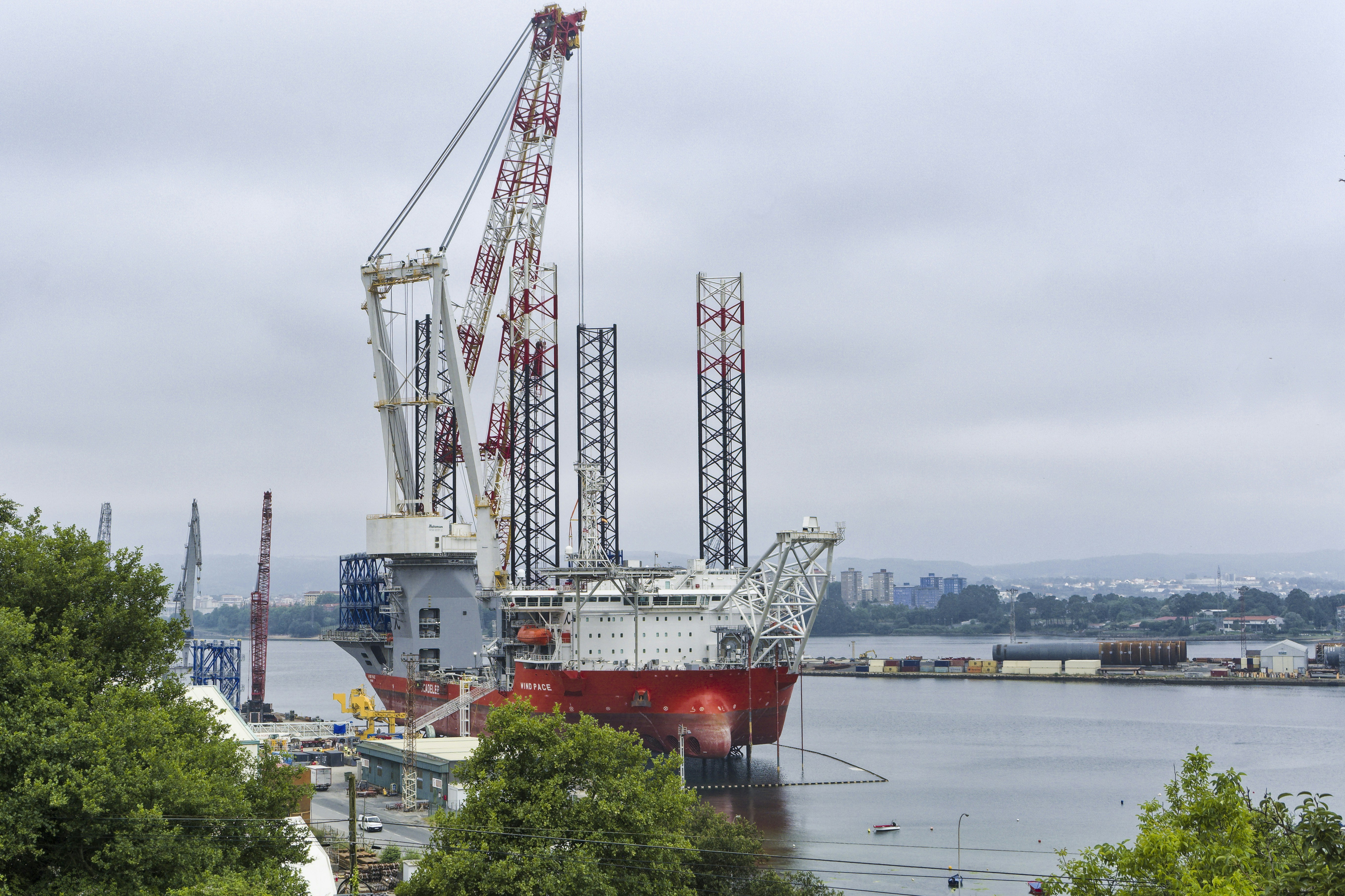 A large offshore drilling rig stands prominently in a harbor, surrounded by cranes and vessels, showcasing the scale and complexity of maritime engineering.