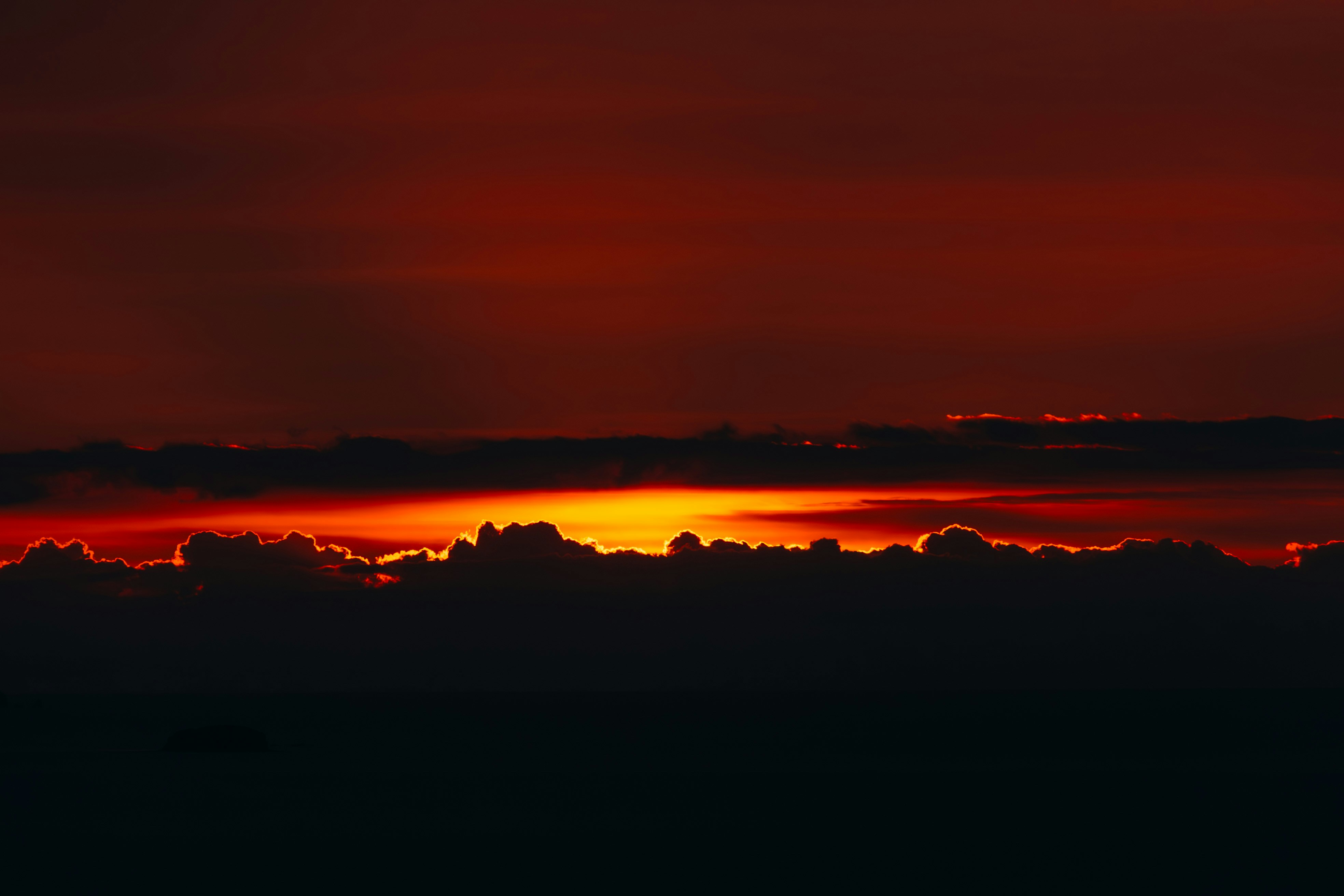 Vivid sunset illuminating the horizon with fiery hues, contrasting against dark clouds. The scene evokes a sense of tranquility and wonder.