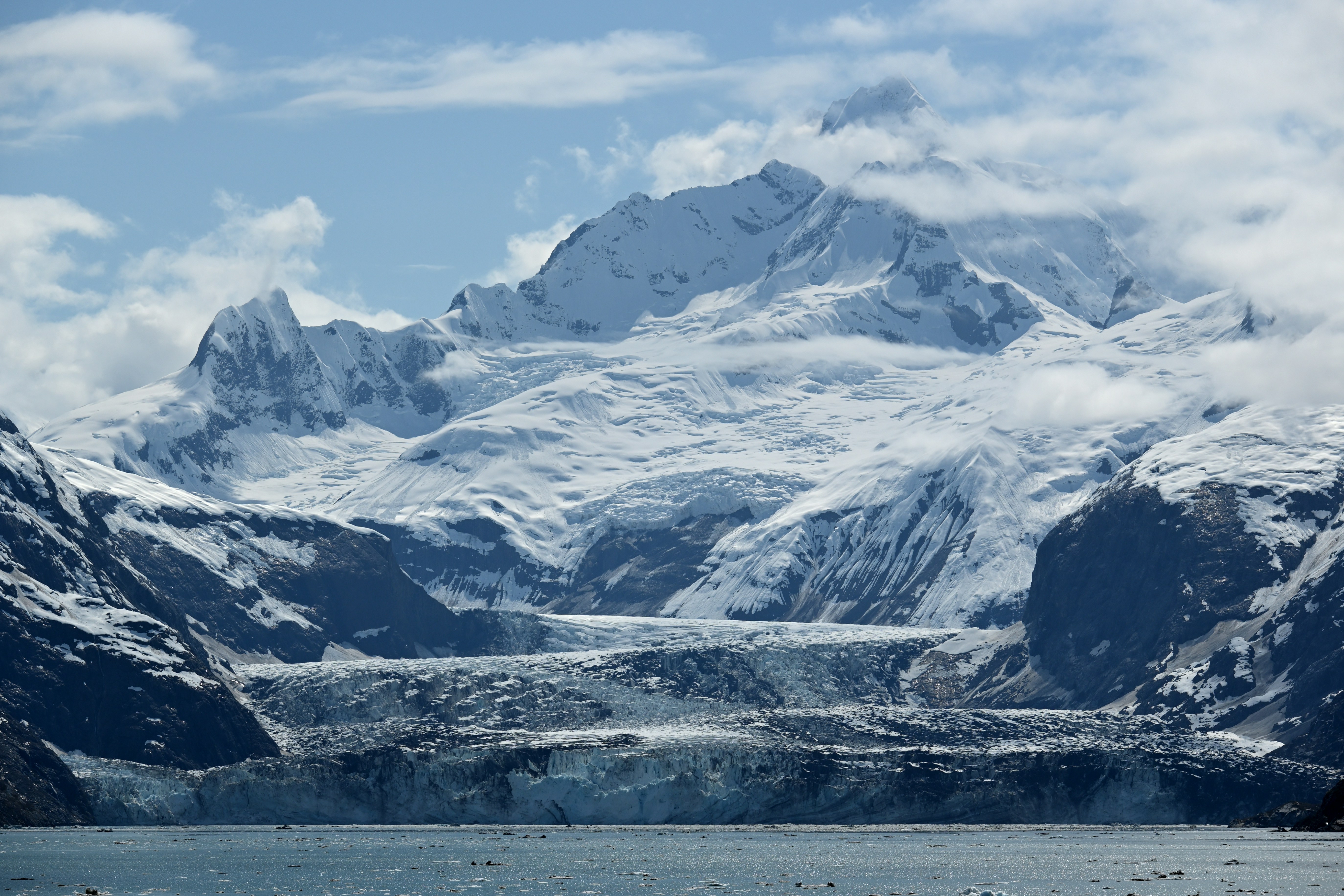 A dramatic view of towering snow-covered mountains and the massive tidewater glacier flowing into the bay in Glacier Bay National Park, Alaska. This untouched wilderness captures the raw beauty of the Arctic and the ever-changing landscape shaped by ice. | A snow-covered mountain and glacier.