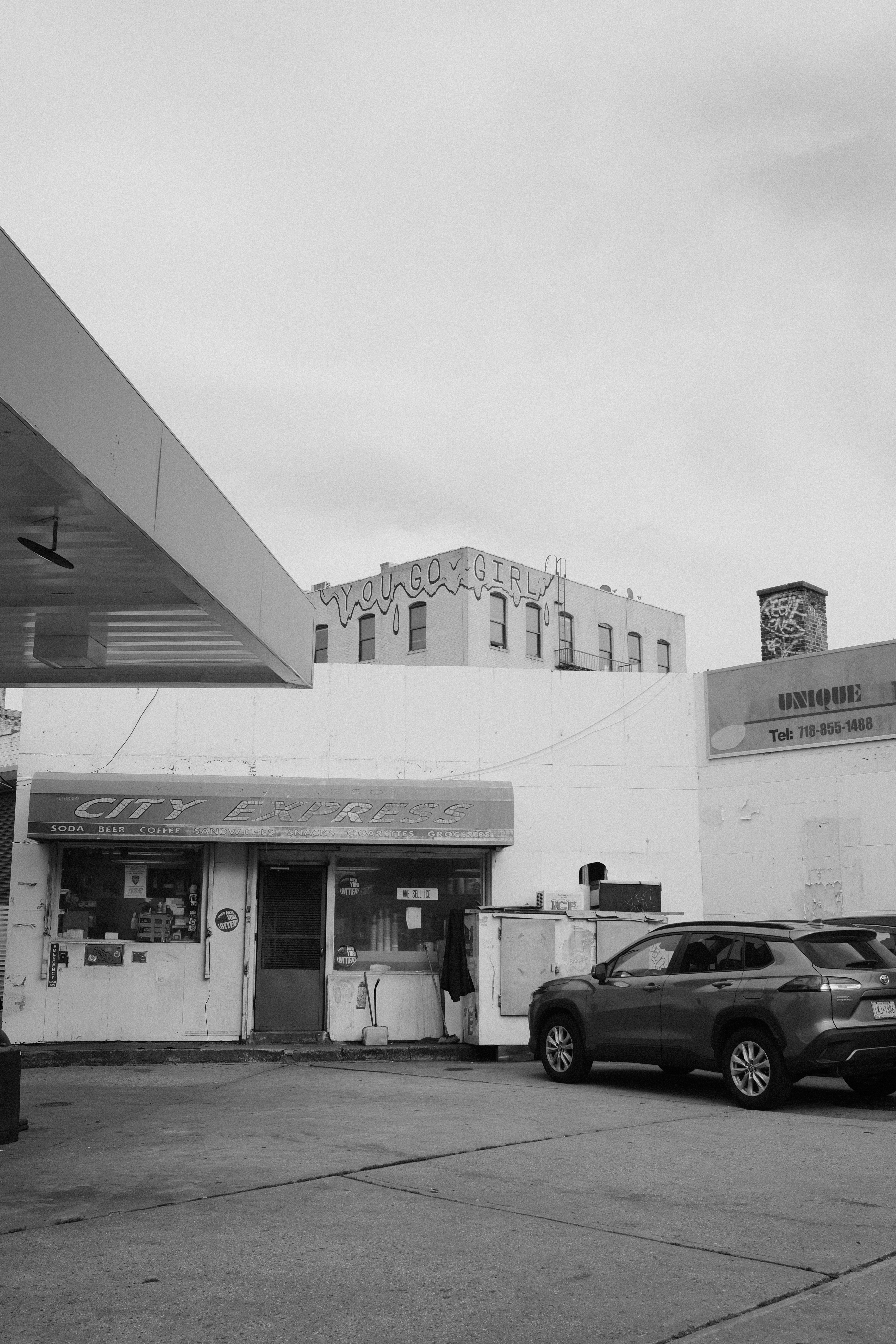 A vintage gas station and convenience store juxtaposed against a faded building with neon signage. The scene captures the essence of urban decay and nostalgia.