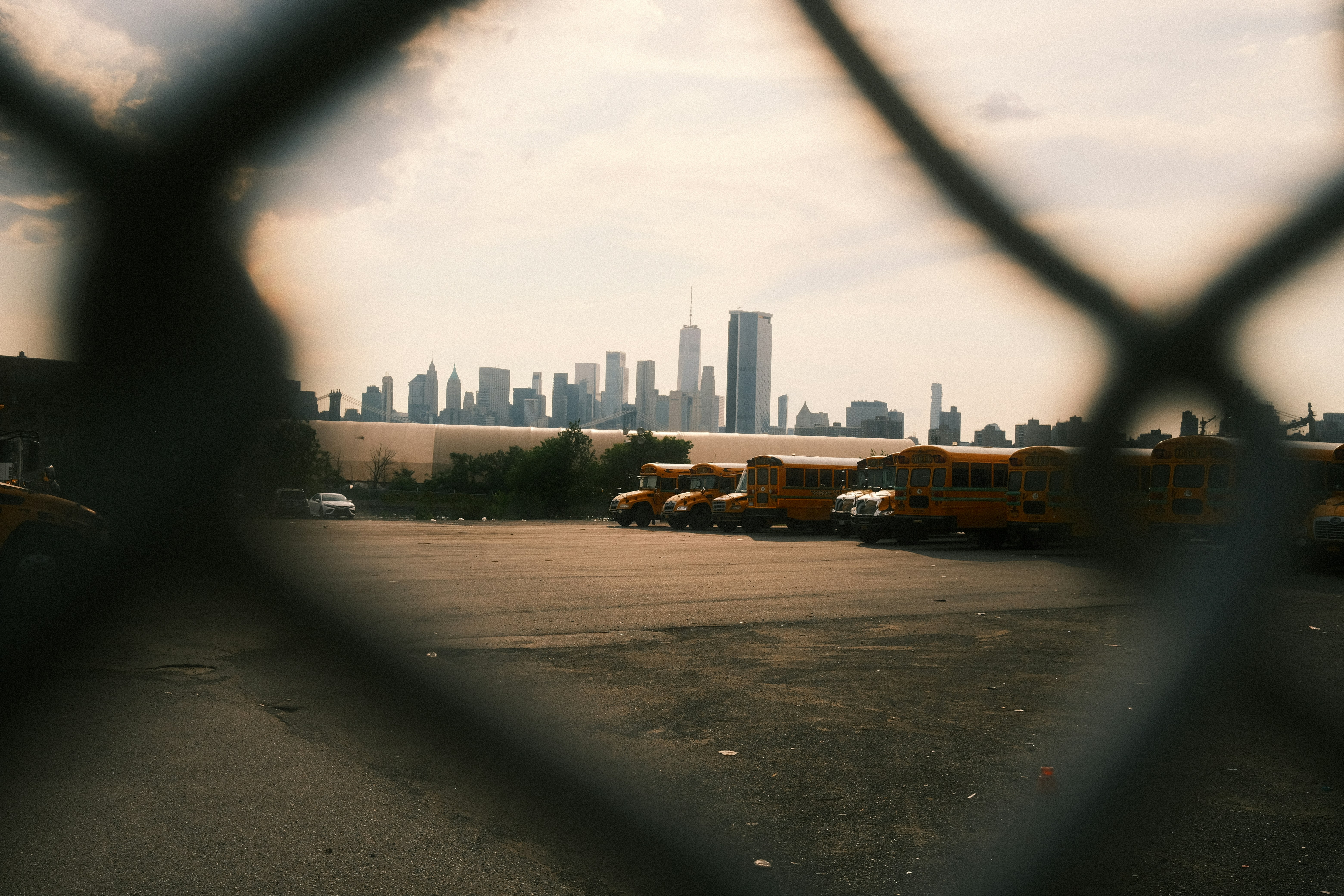 Through a Fence, the City Rises: Distant Towers Beyond a Yard of Buses