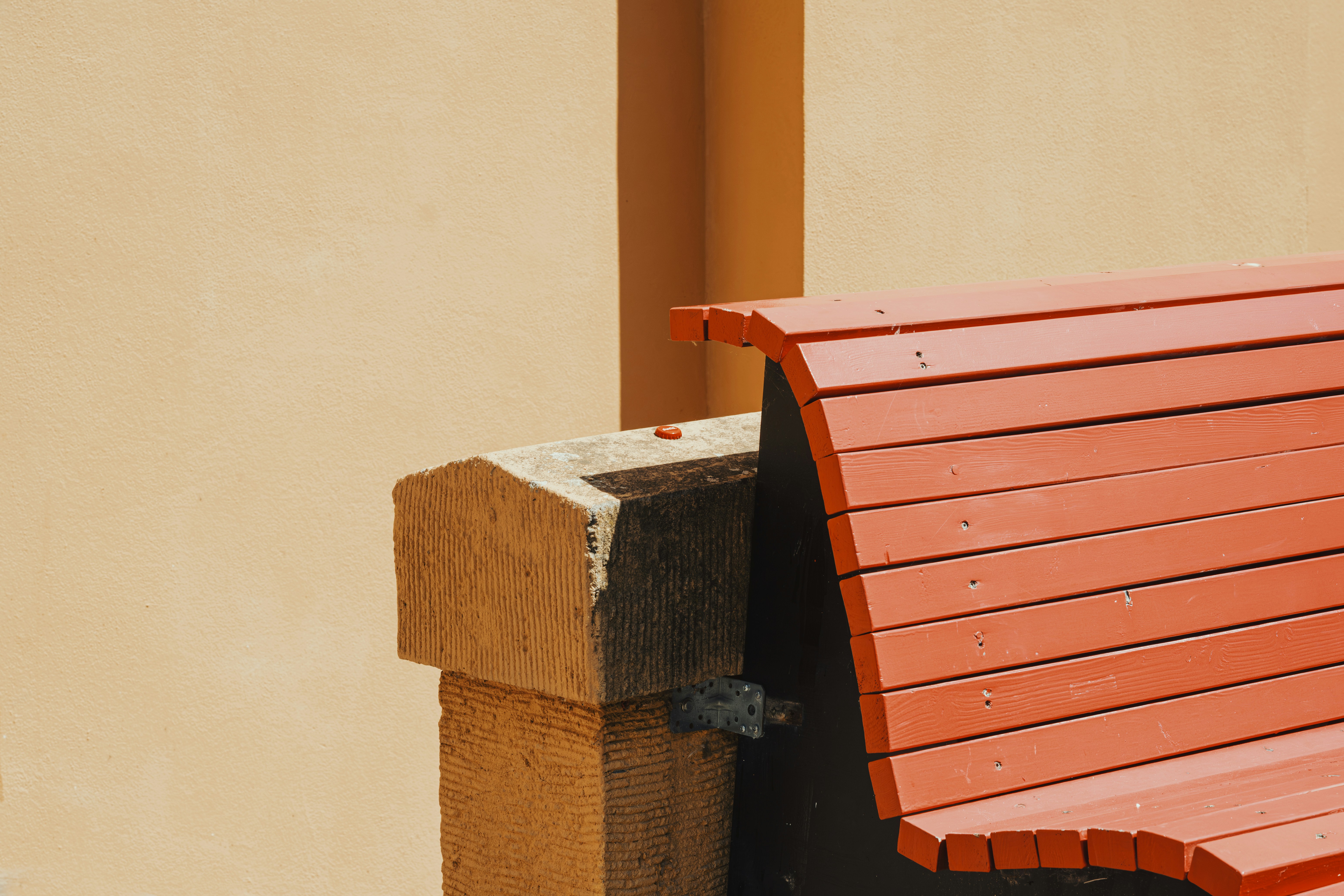 Red wooden bench with a curved top against a smooth beige wall, highlighting the contrast of materials and colors.