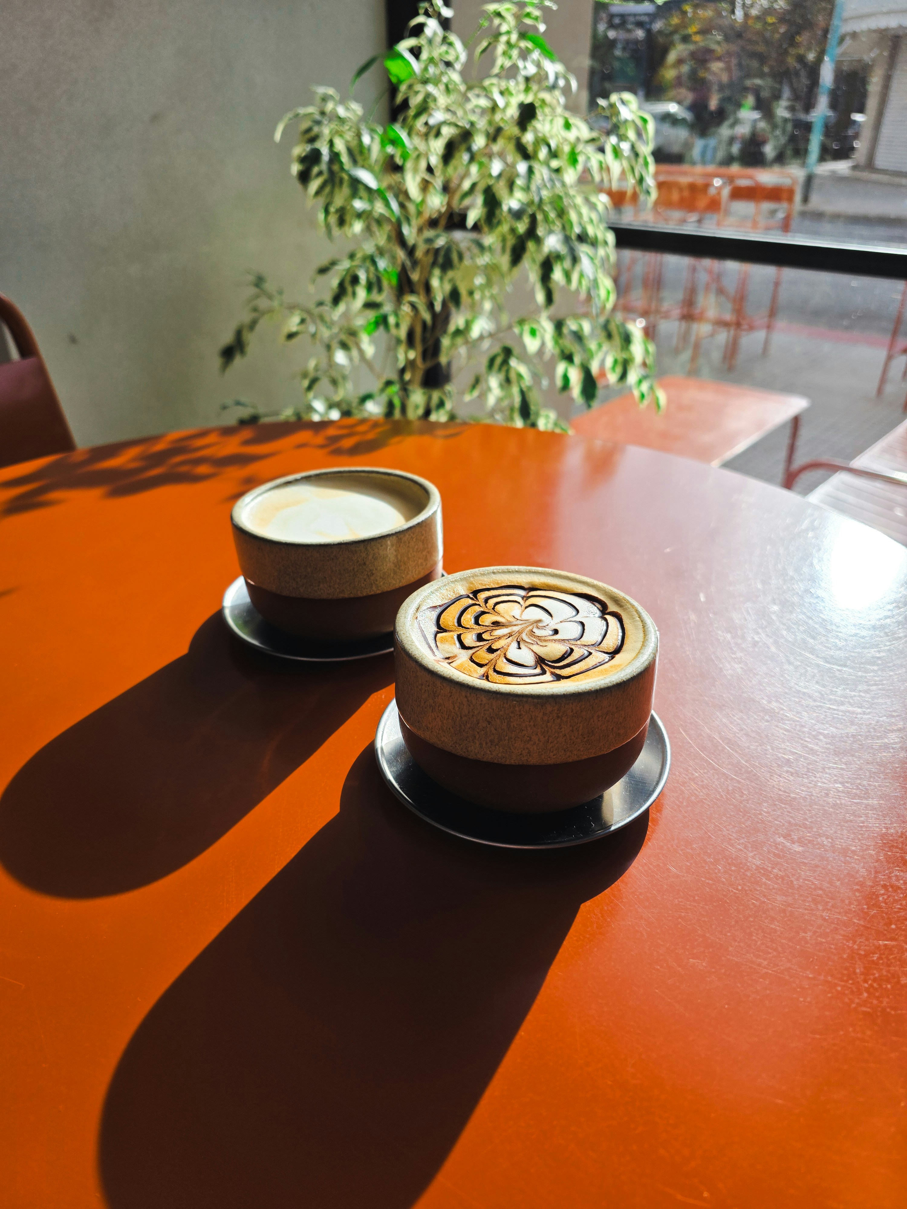 Two coffees sit on a sunny, orange table.