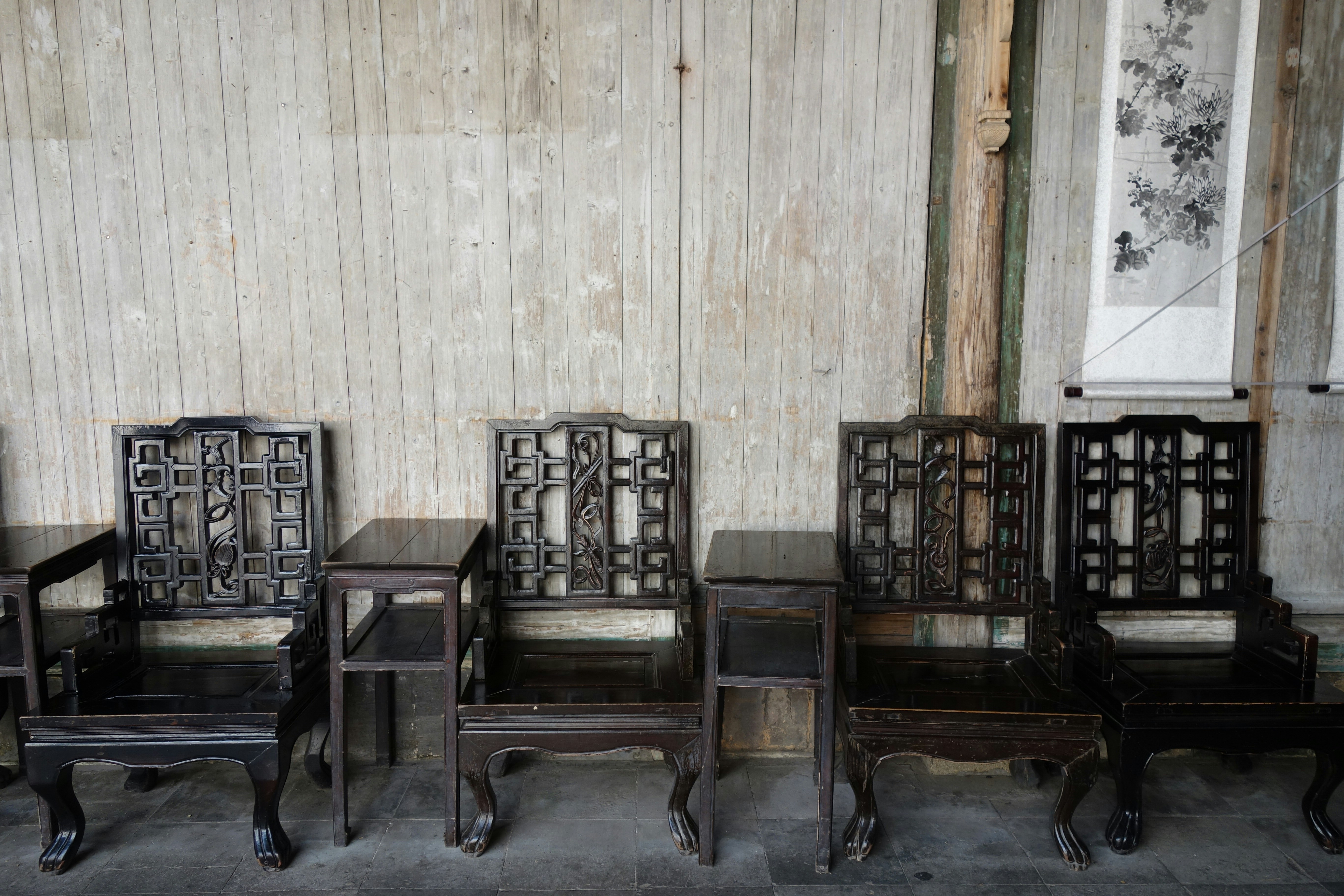 Six Carved Chairs Stand in Quiet Patina Along a Weathered Wall