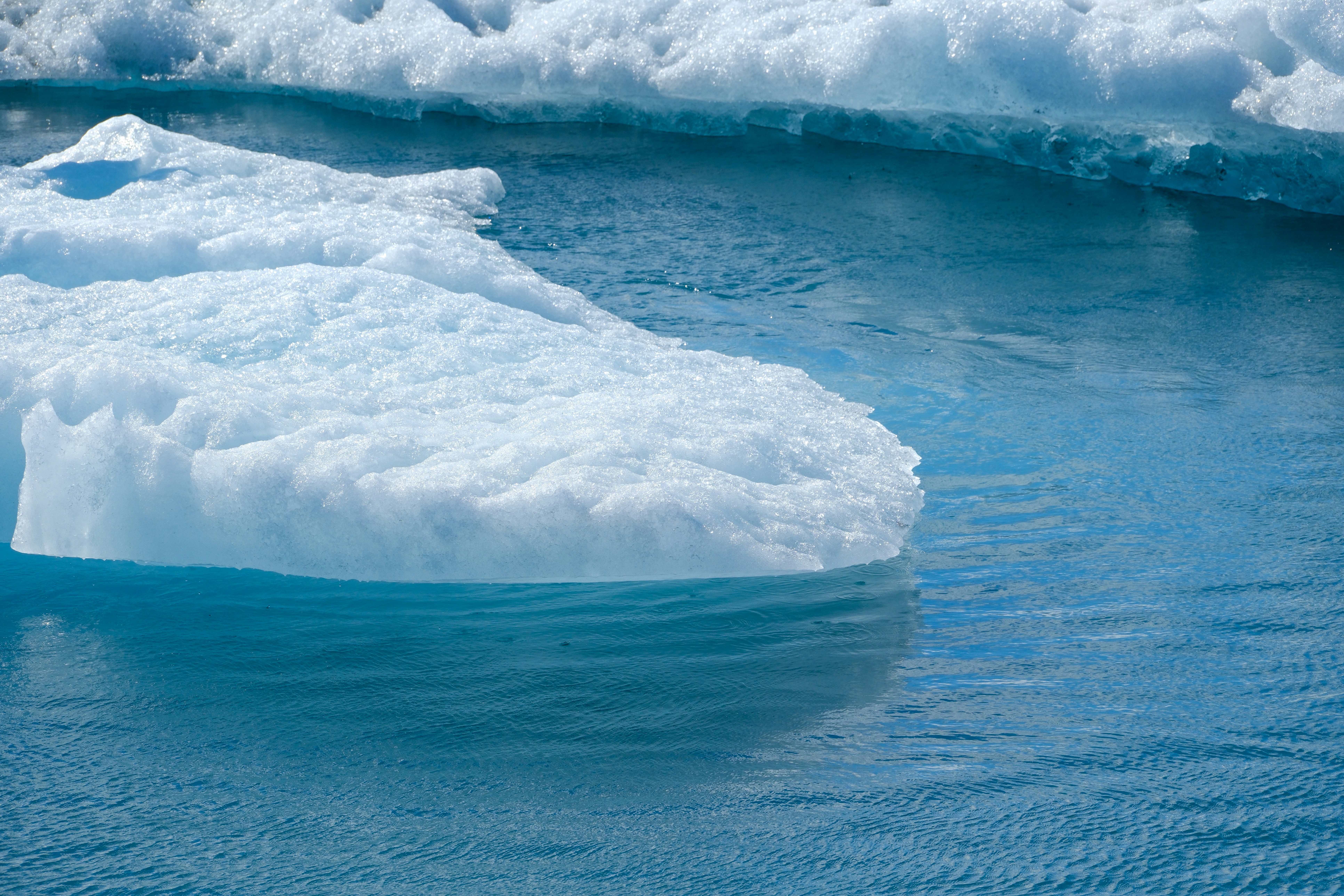 Iceberg floating serenely on clear blue waters, showcasing the contrast between the white ice and the vibrant aquatic hues.