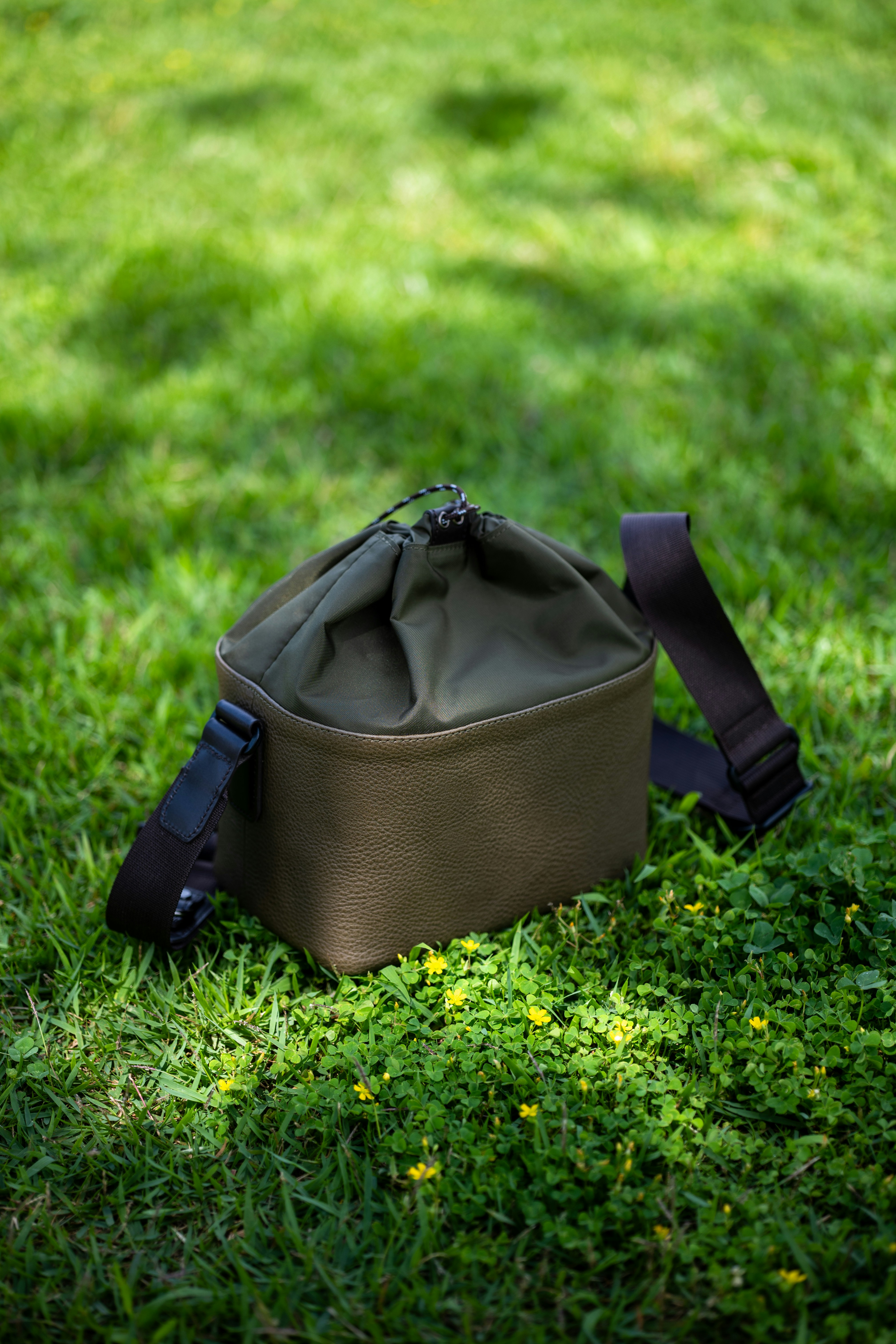Stylish camera bag resting on lush green grass, highlighting its earthy tones and practical design.