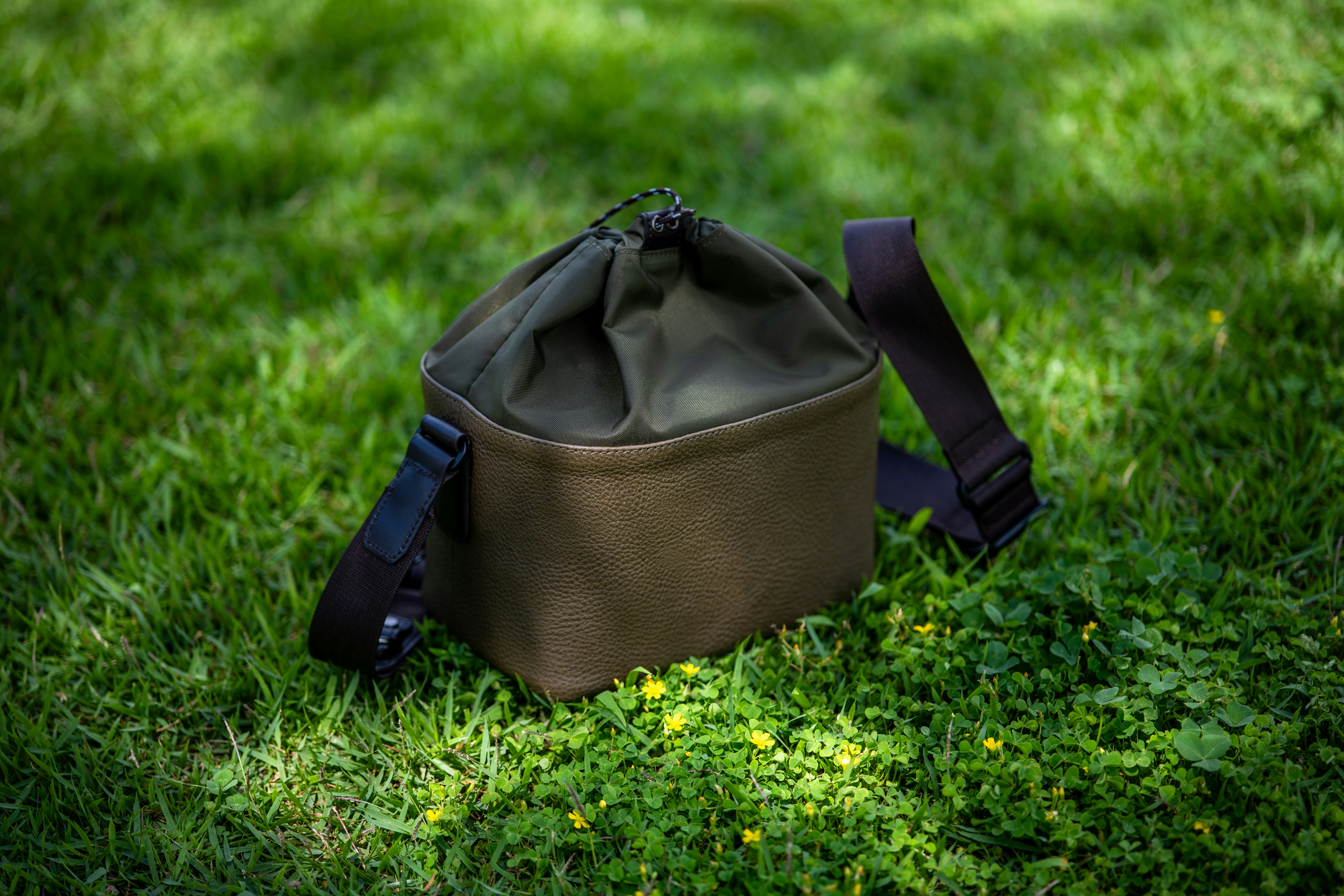 A green bag sits in the sunny green grass.