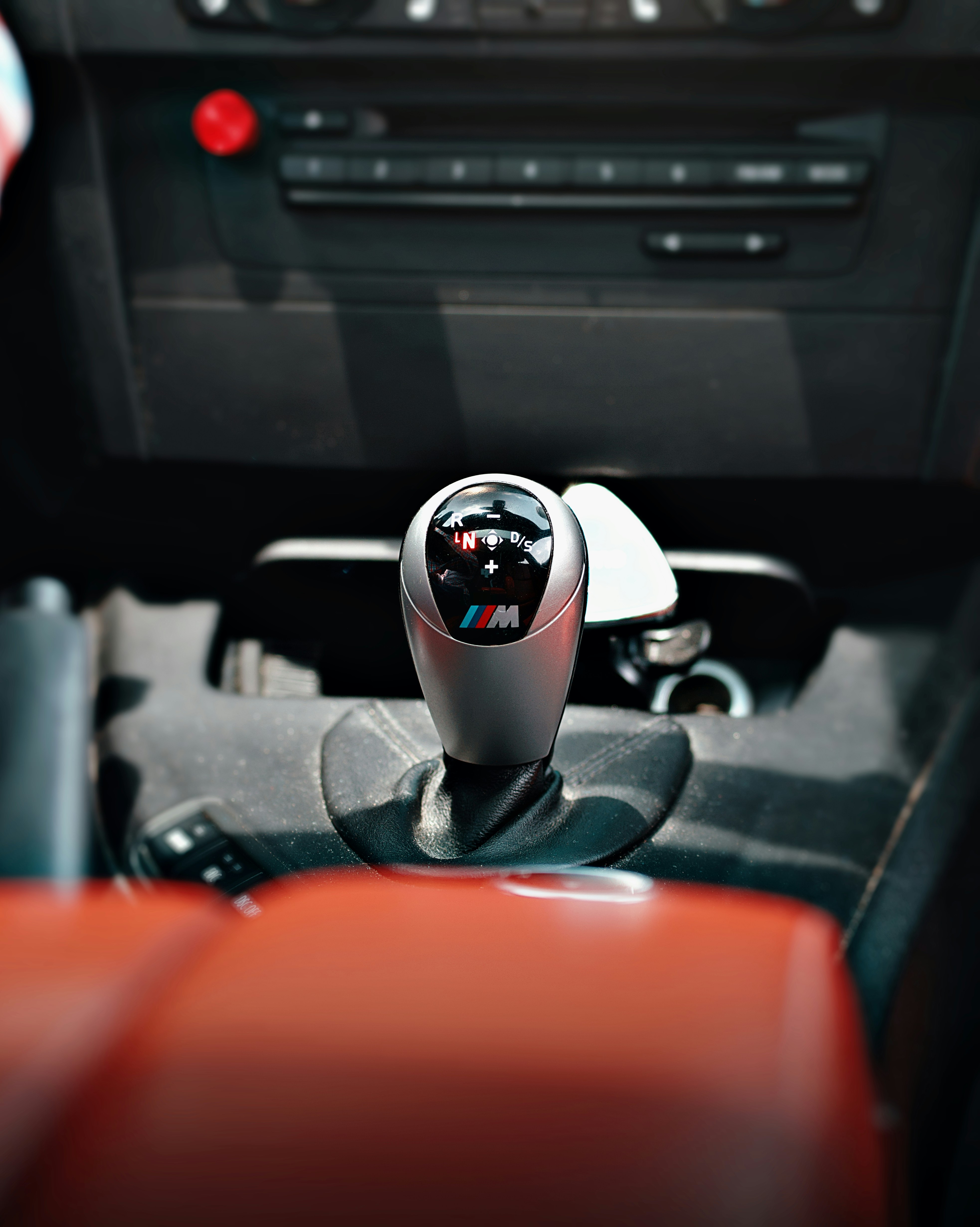 M Badge Lever: Close-Up of a Metallic Gear Knob in a Crimson Car Cabin