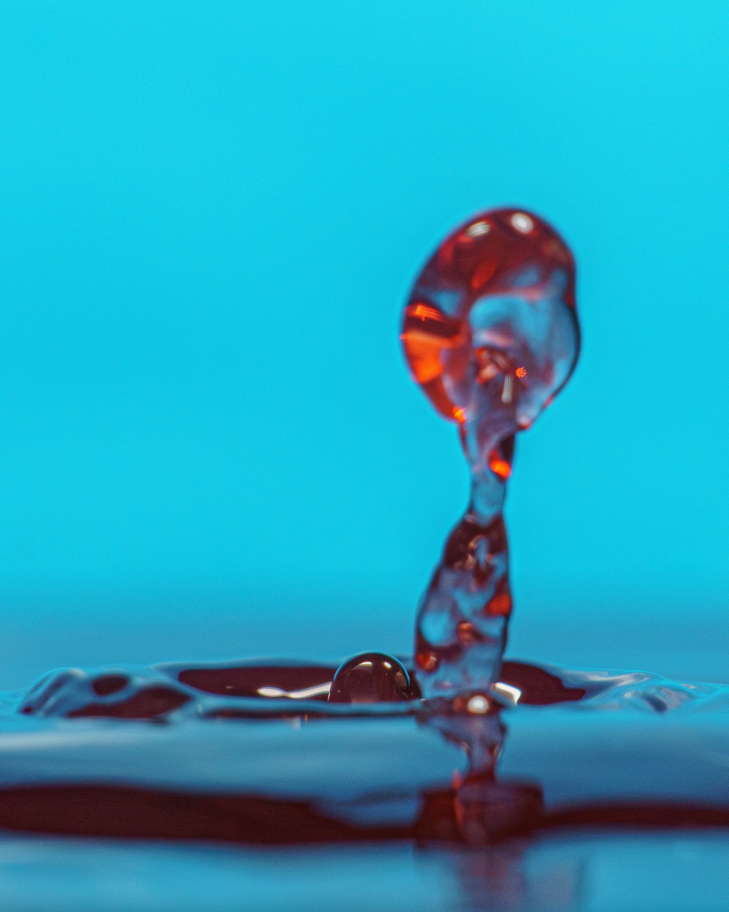A vibrant splash of red liquid forming a delicate droplet against a turquoise background, capturing the moment of impact. The image showcases the beauty of fluid dynamics.