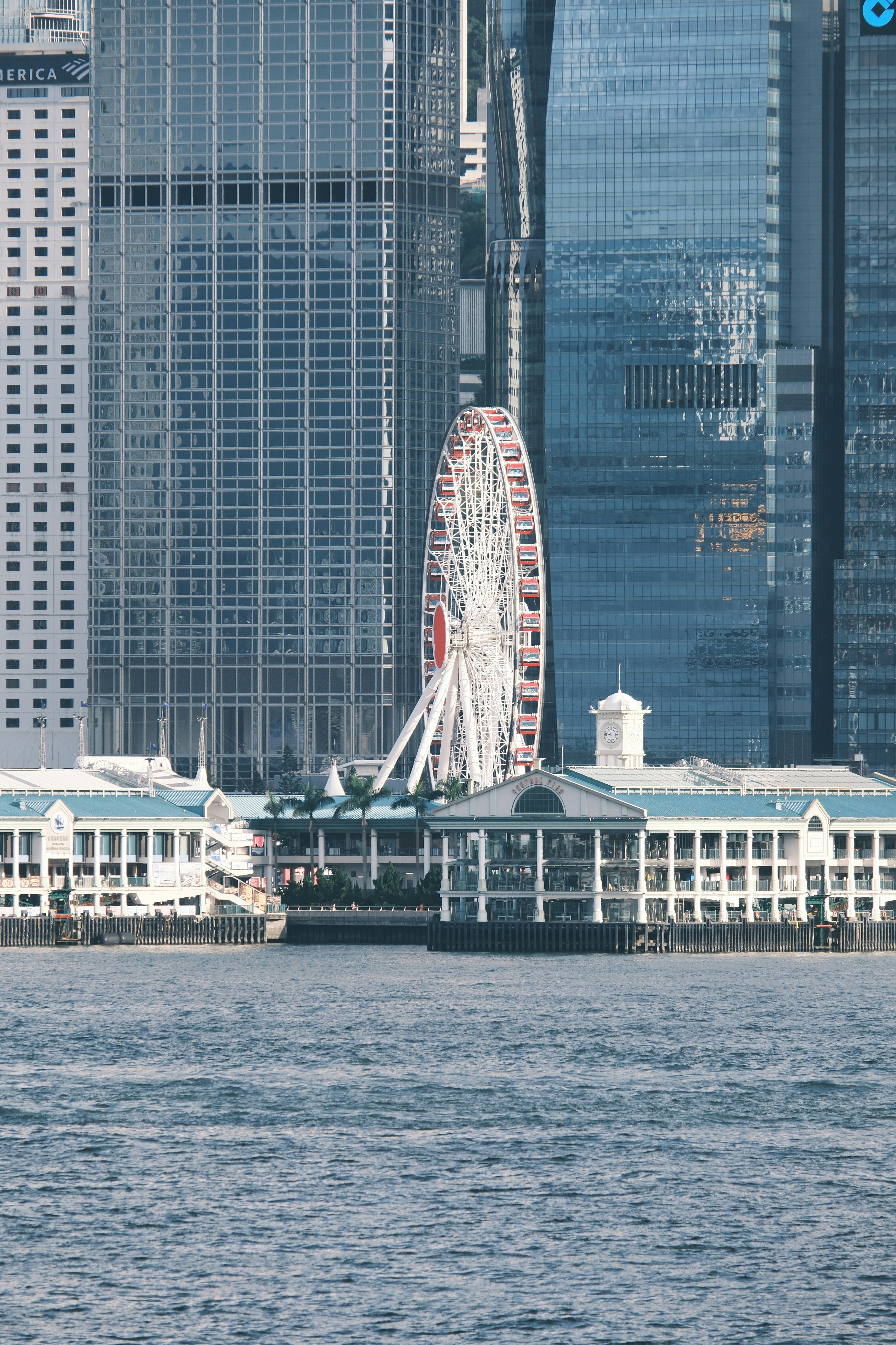 A vibrant Ferris wheel stands in contrast to towering skyscrapers, embodying the blend of leisure and urban life. The waterfront structure adds to the city's charm.