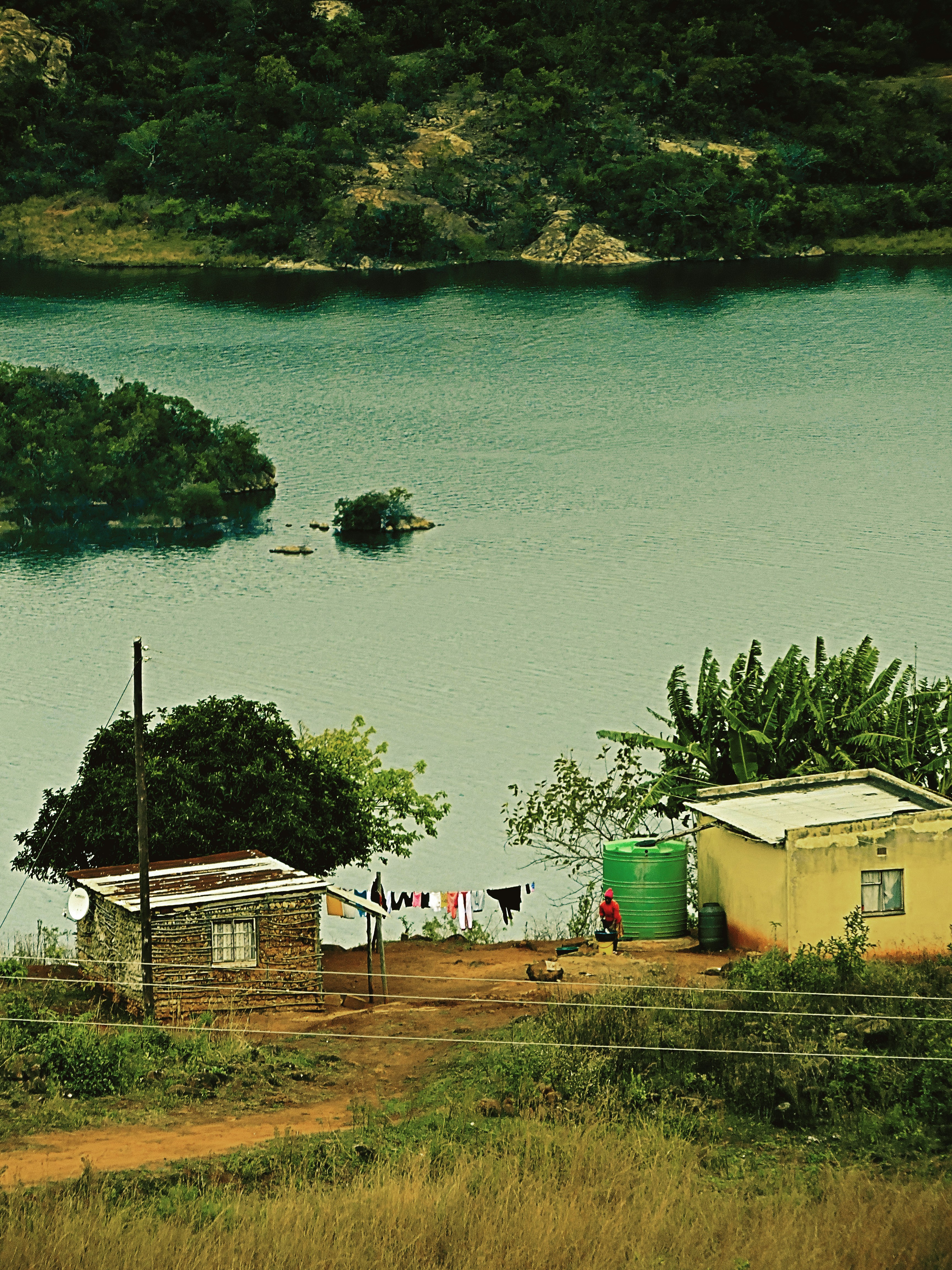 A rustic homestead near a tranquil lake, with laundry hanging in the breeze and lush greenery surrounding the scene.
