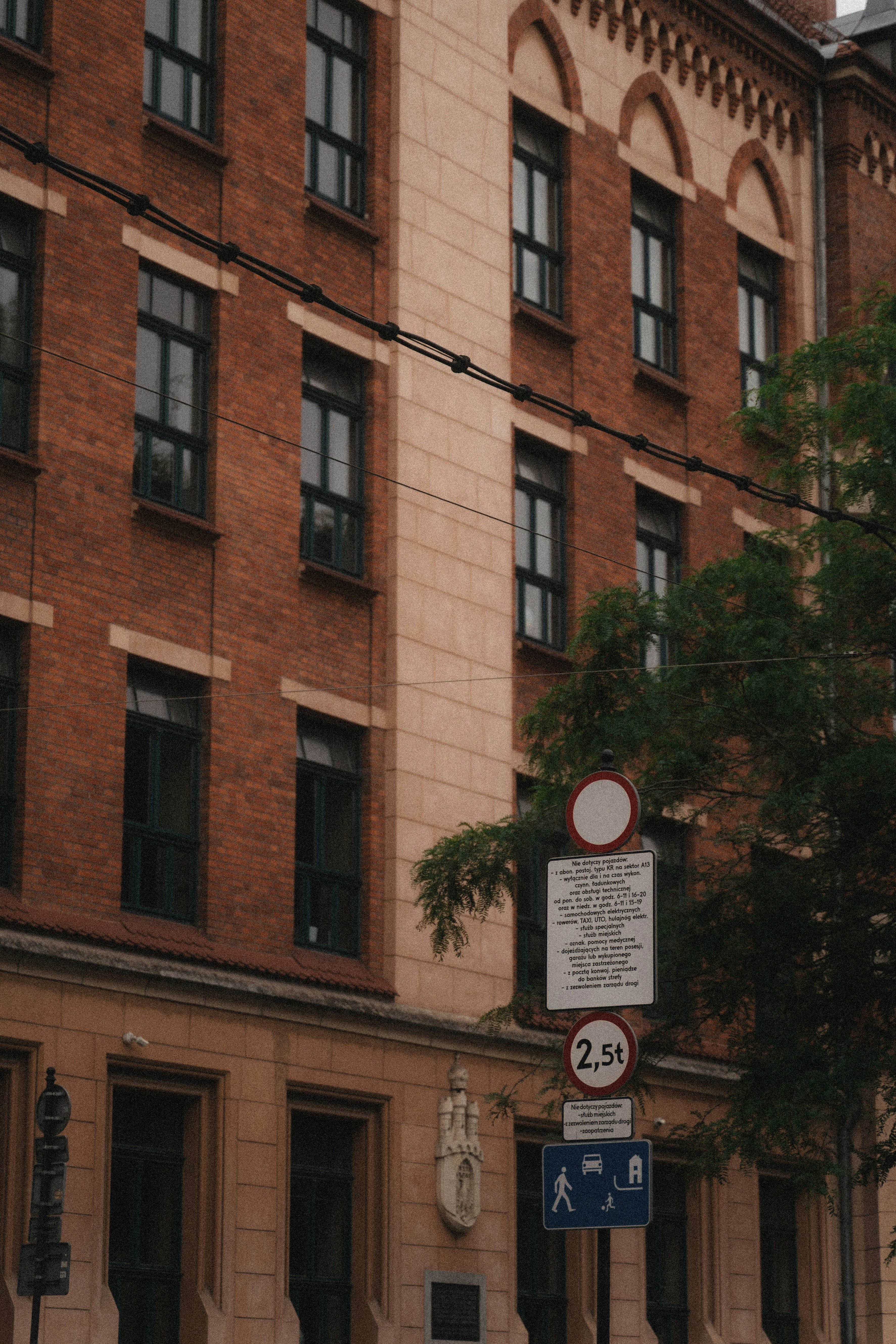 An intricate brick facade featuring large windows, complemented by street signs and greenery, capturing urban life in a historical context.