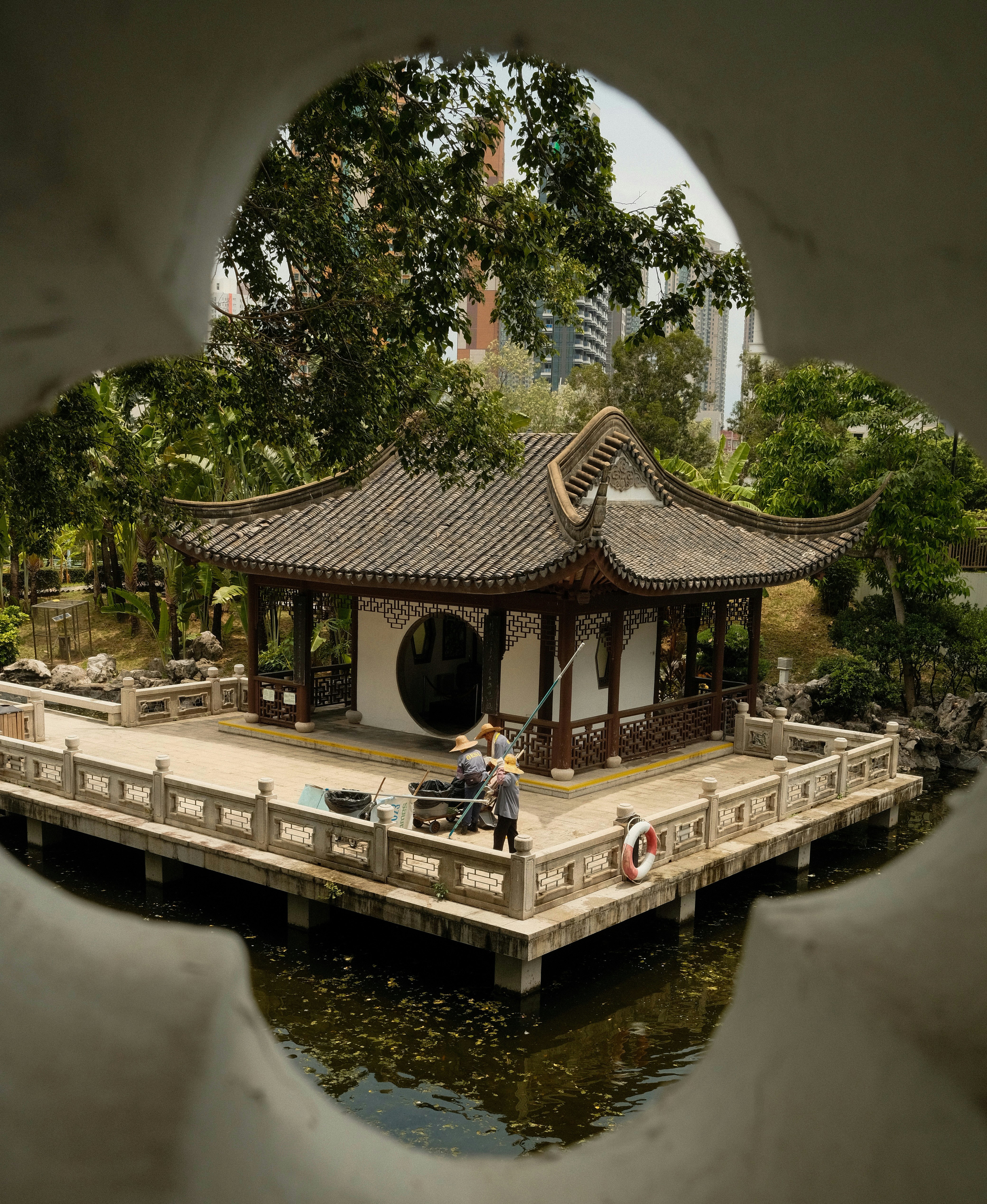Traditional Chinese pavilion surrounded by lush greenery and water, viewed through a stone archway.