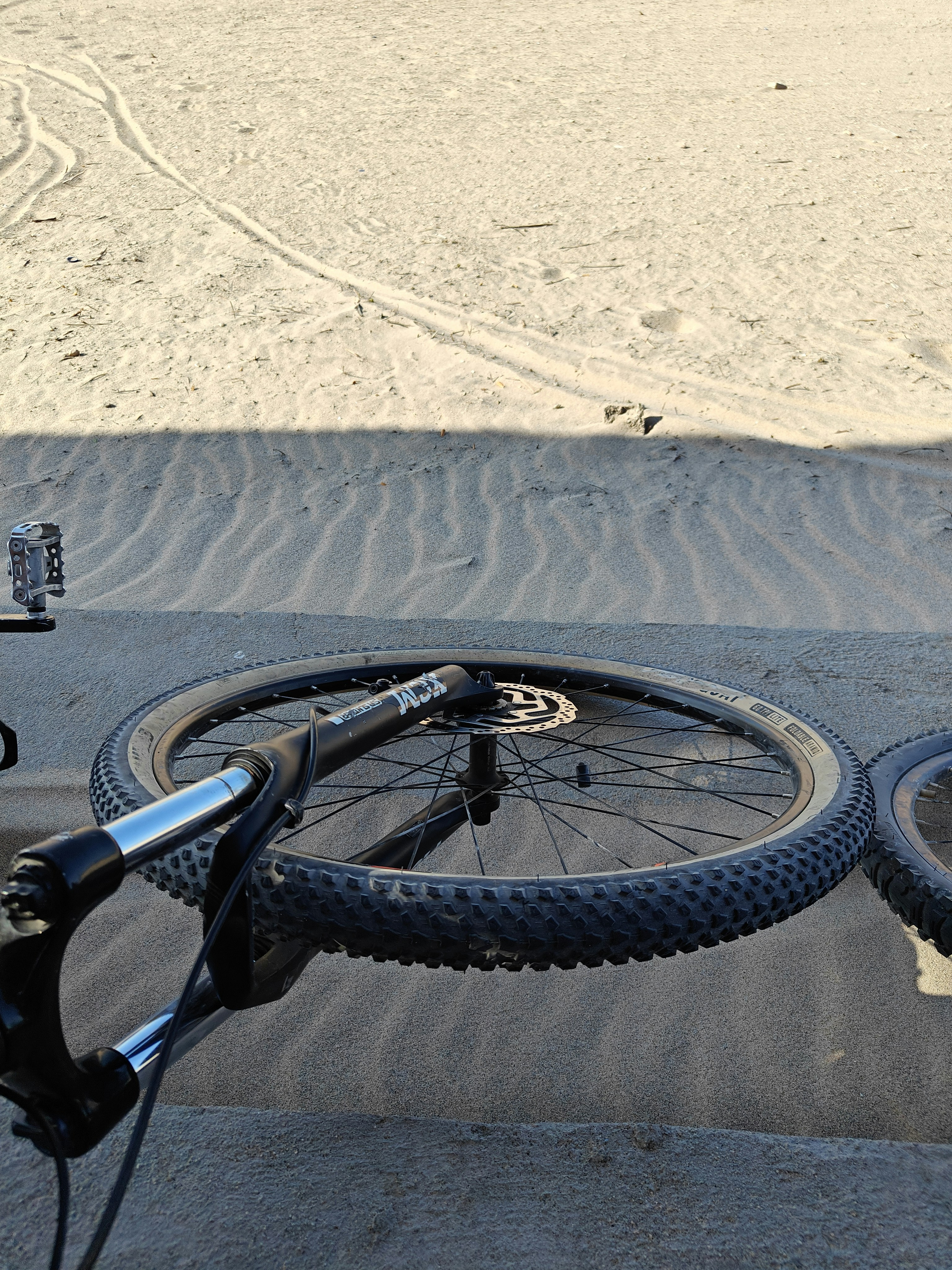 Shadowed Wheels by the Curb: A Bicycle Paused Against a Sandy Backdrop