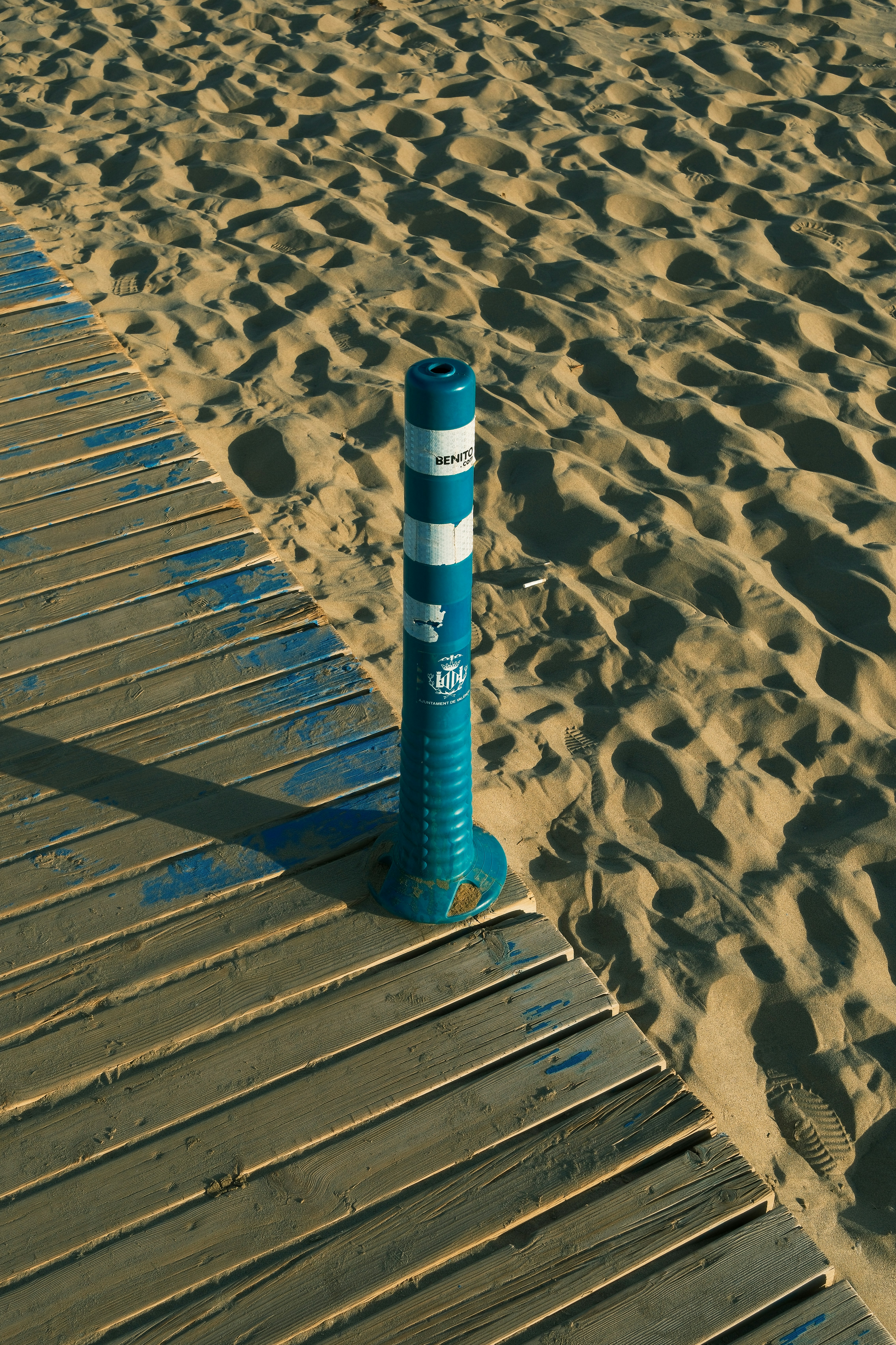 Blue Post on a Sunlit Beach Boardwalk: Texture, Shadow, and Sand