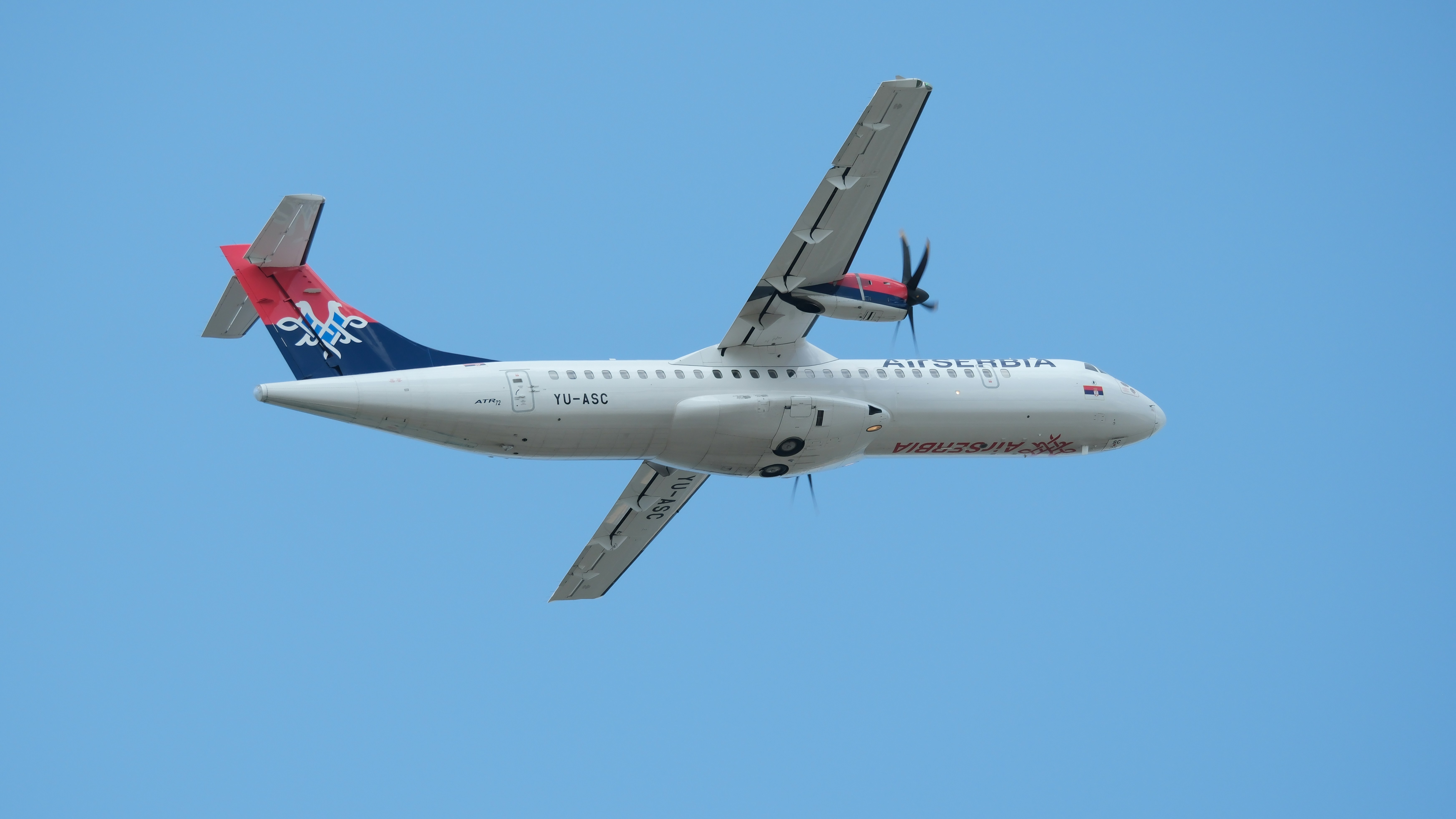 A turboprop aircraft in flight against a clear blue sky, showcasing its aerodynamic design and vibrant livery.