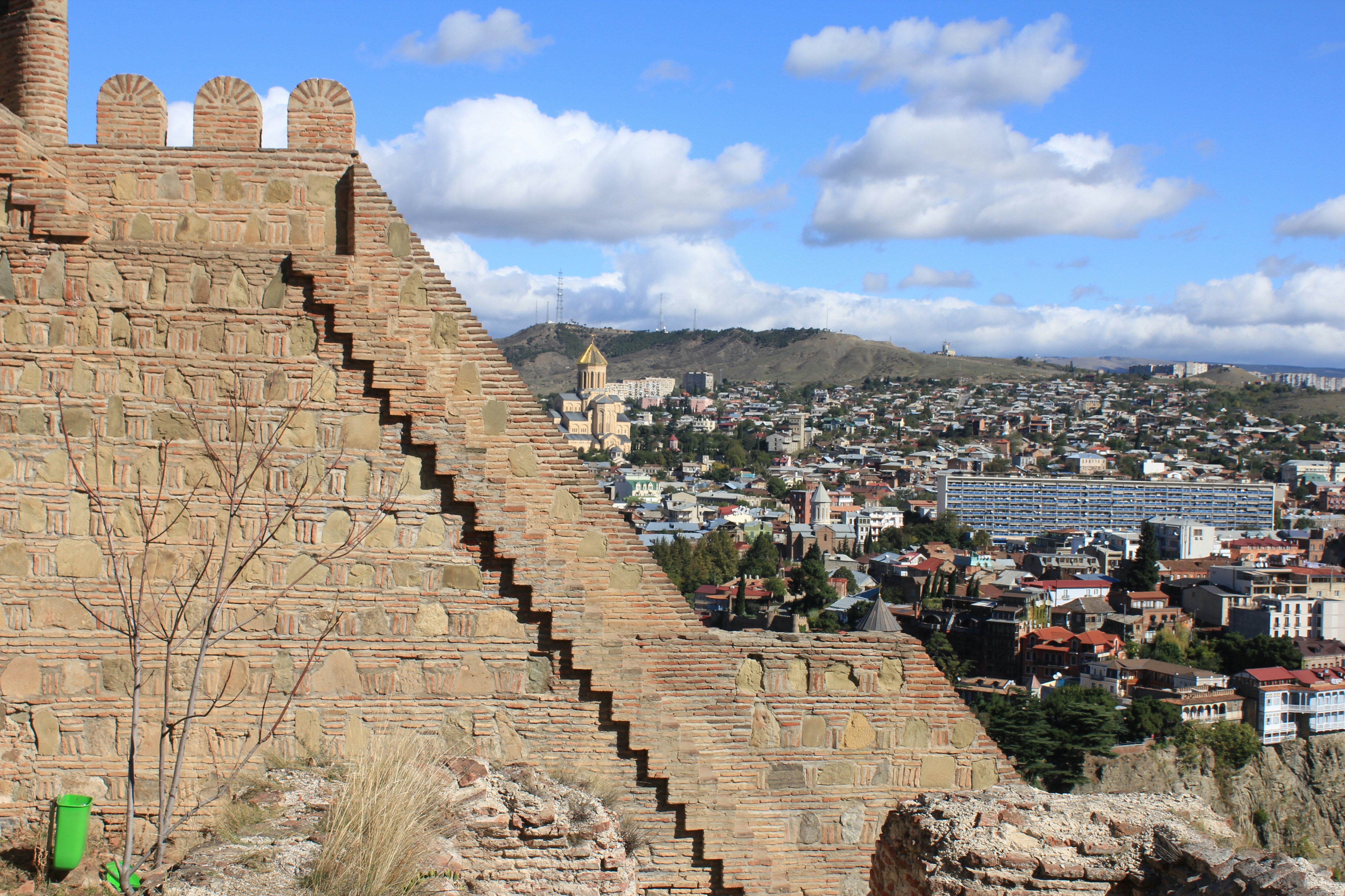 Ancient stone staircase leading down toward the cityscape of Tbilisi, with a blend of historic architecture and modern buildings under a bright blue sky.