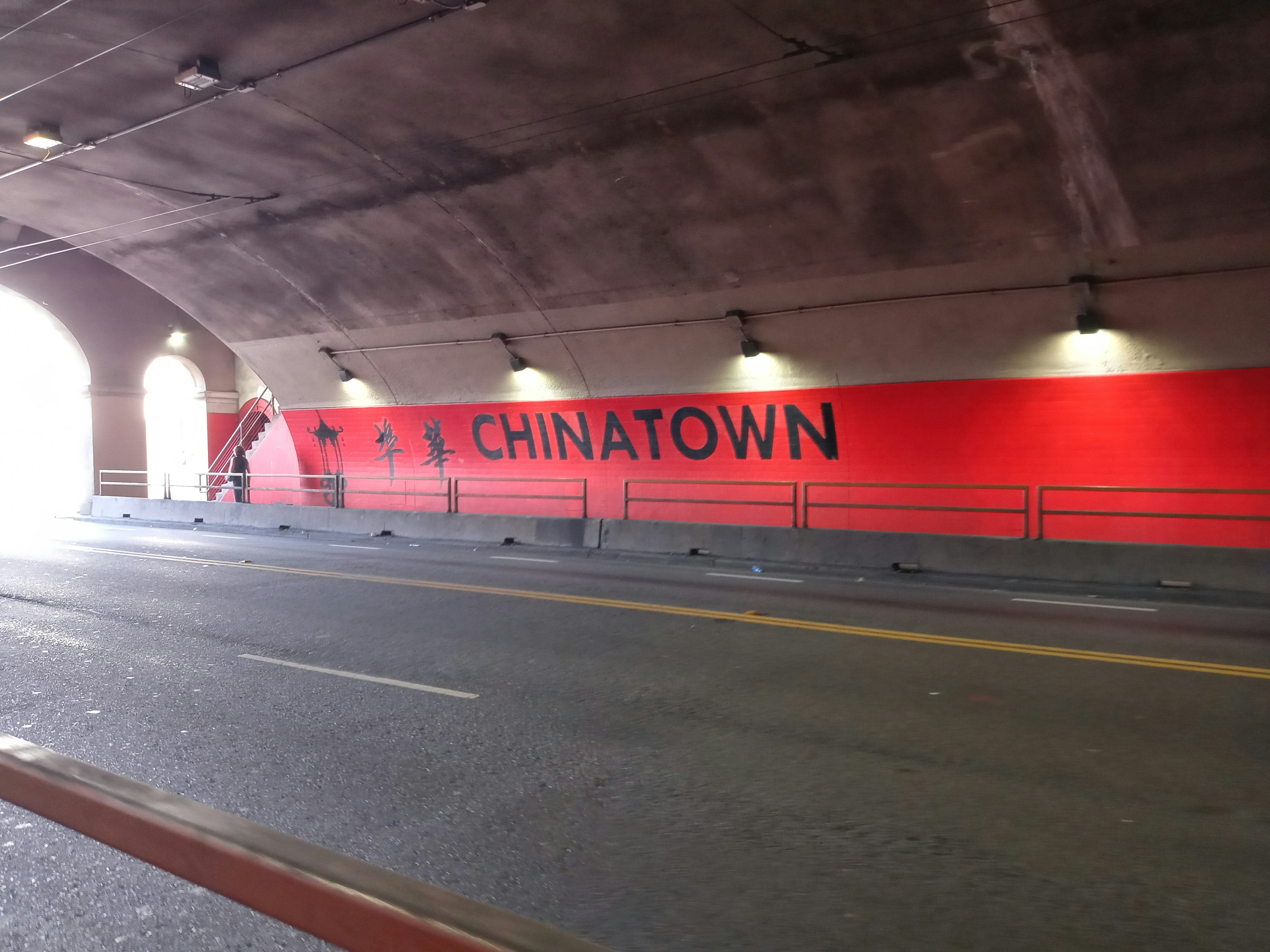 Bold red mural featuring 'CHINATOWN' painted on an urban tunnel wall, with light streaming in from the entrance.