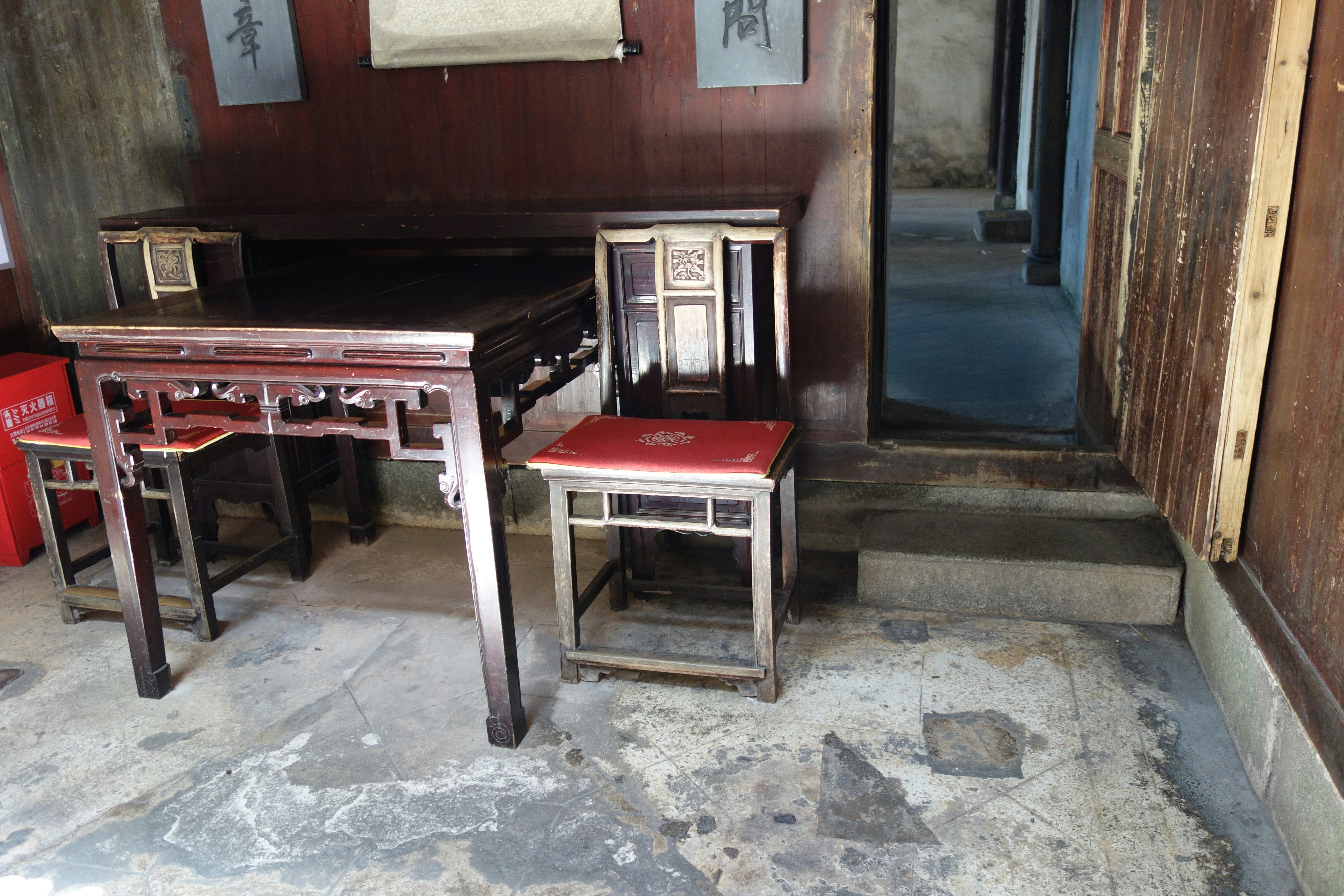 Carved Quiet: A Wooden Shrine Framed by Red Cushions in a Traditional Hall