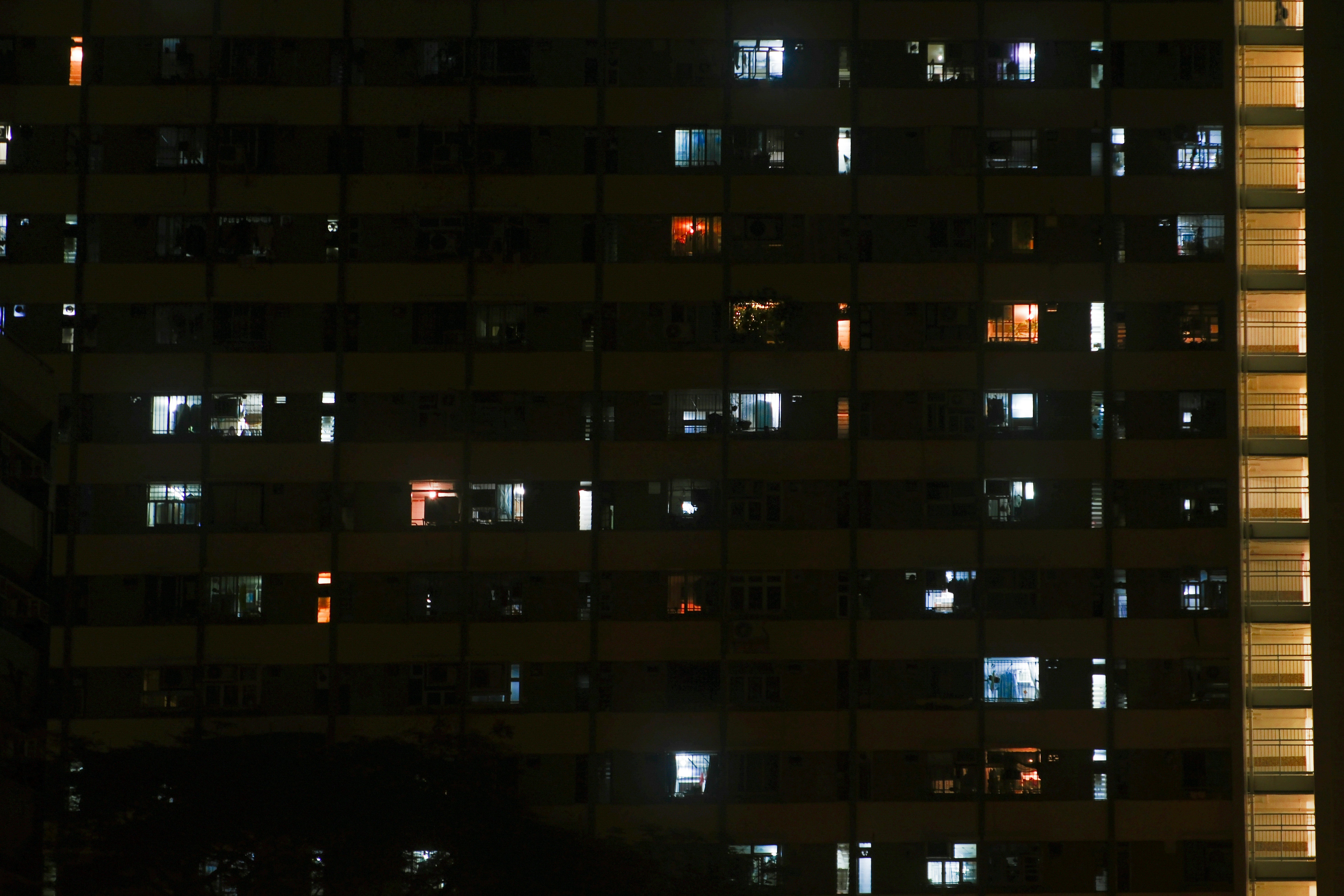 A high-rise building at night, showcasing illuminated windows that hint at the lives within. The contrasting darkness highlights individual stories behind each light.