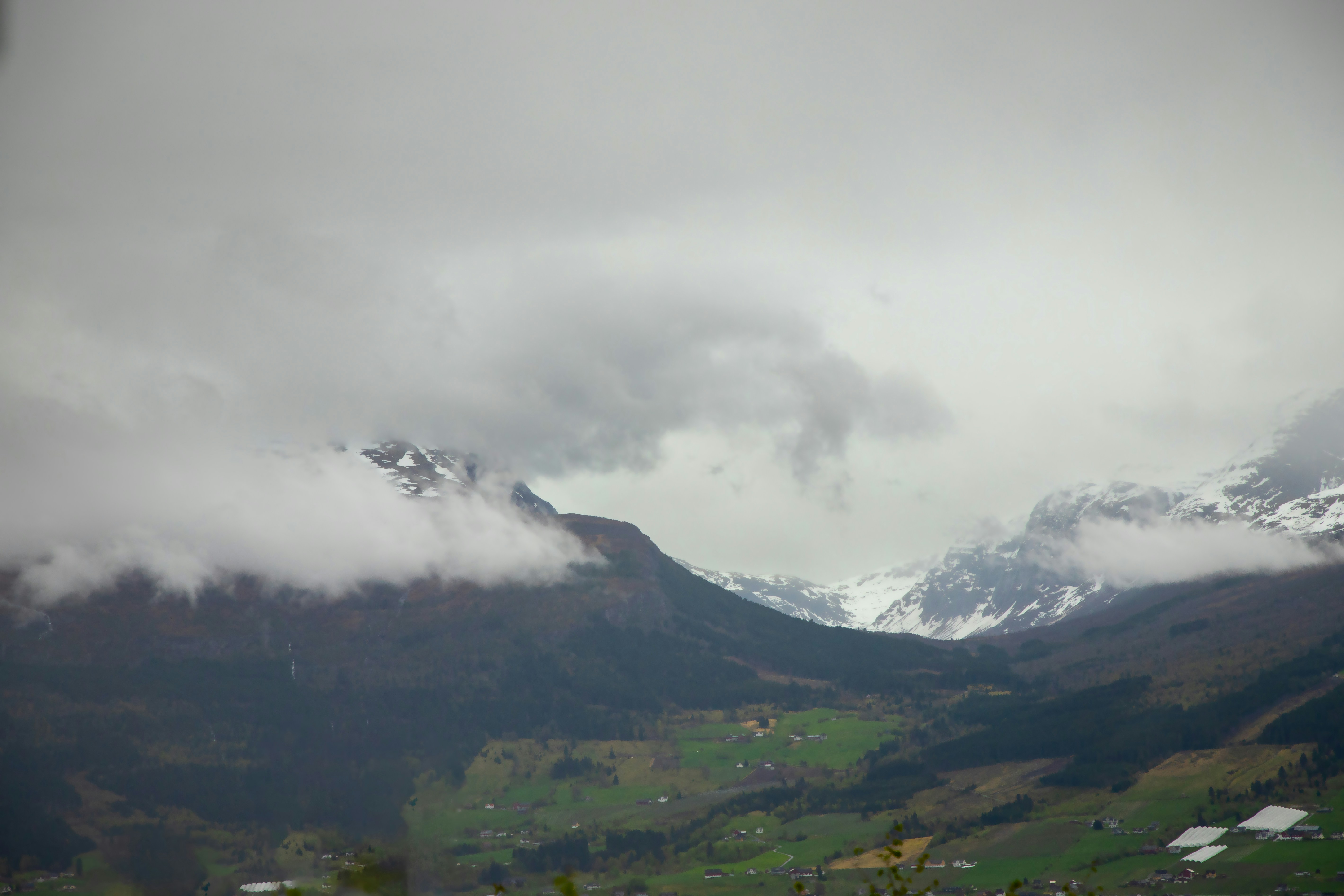 Misty mountains shrouded in clouds, revealing hints of snow-capped peaks and lush green valleys below.