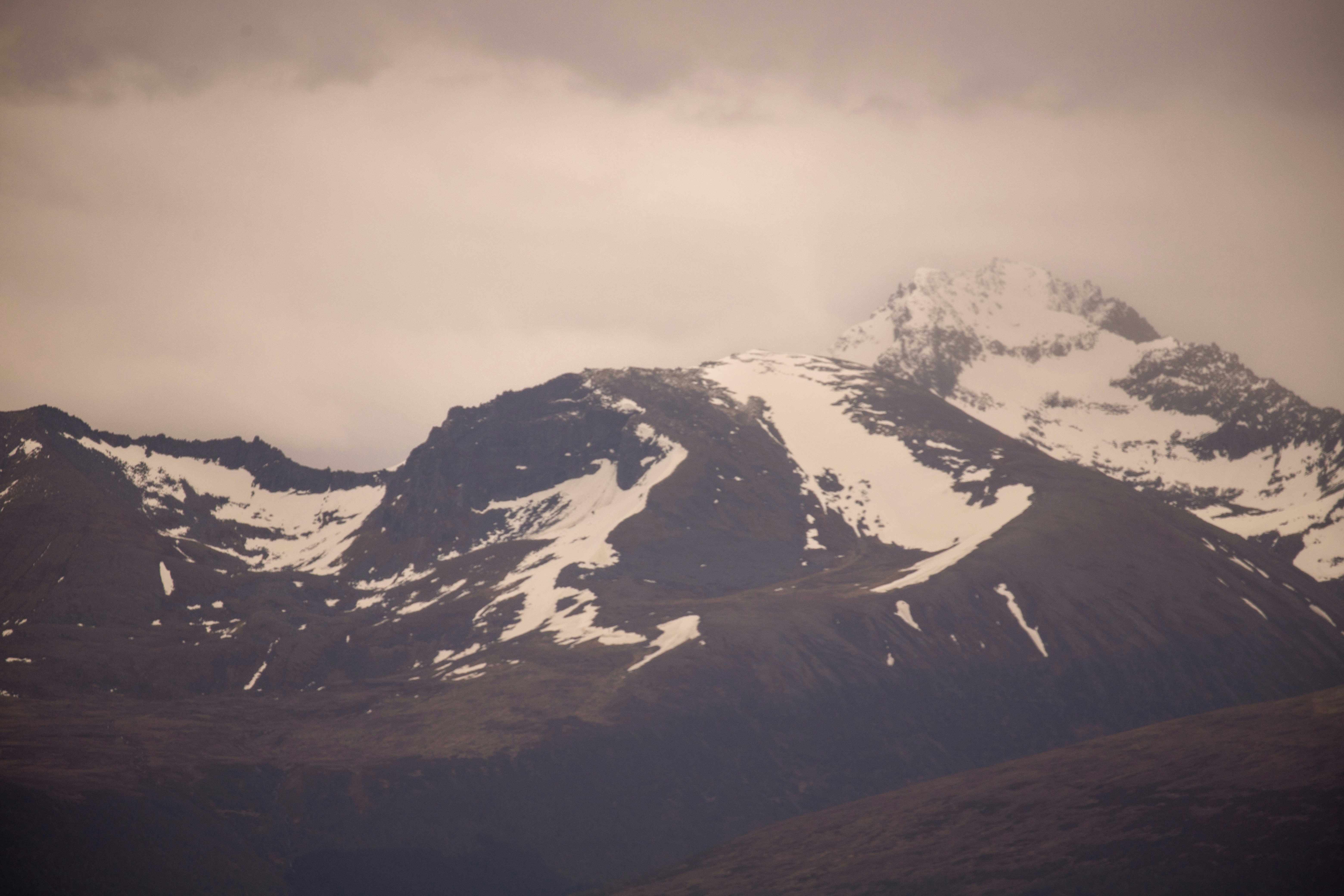 Majestic mountains adorned with patches of snow under a moody sky, showcasing the raw beauty of nature's landscape.