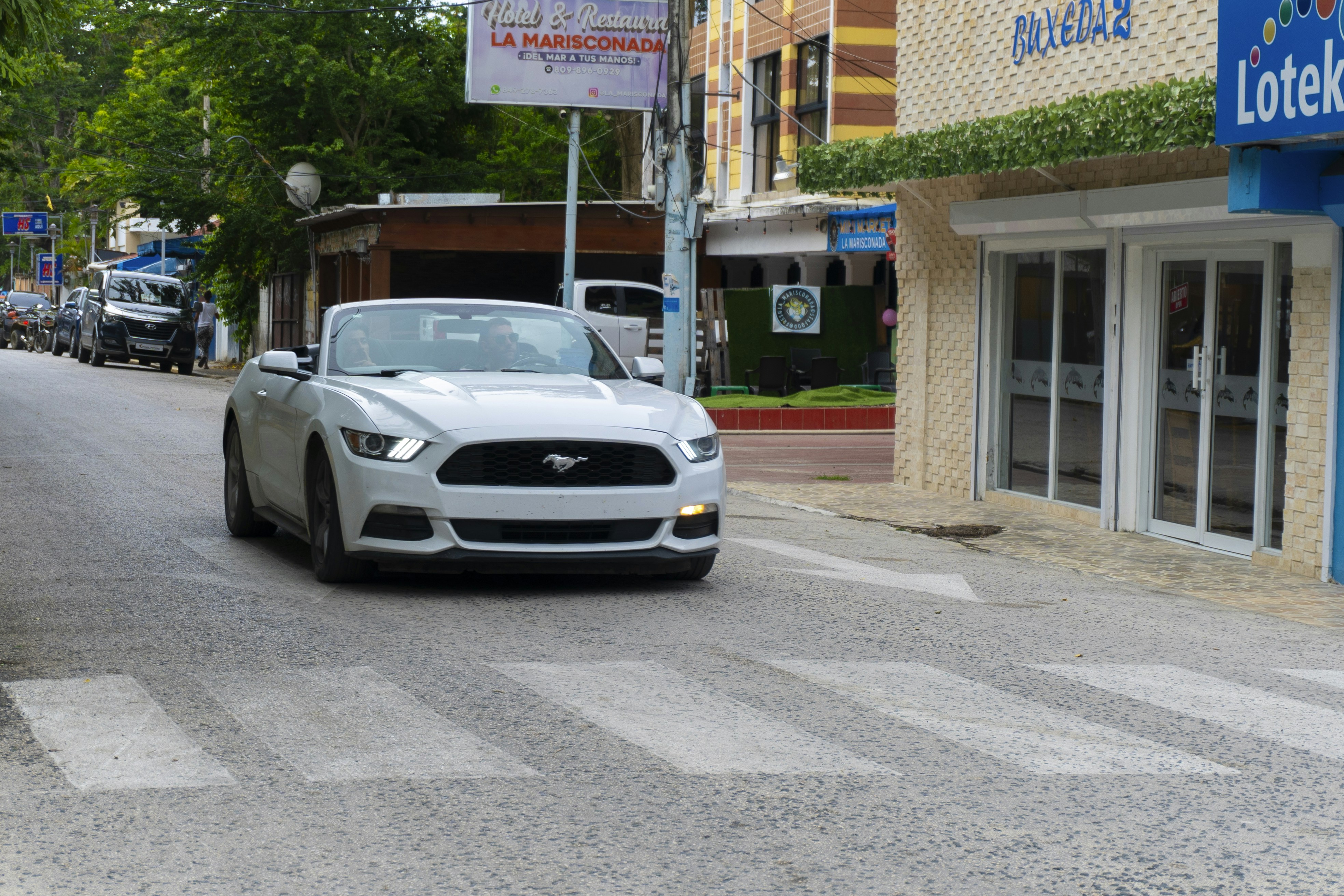 Crosswalk Cruiser: White Mustang Surges Through a Sunlit Town Street