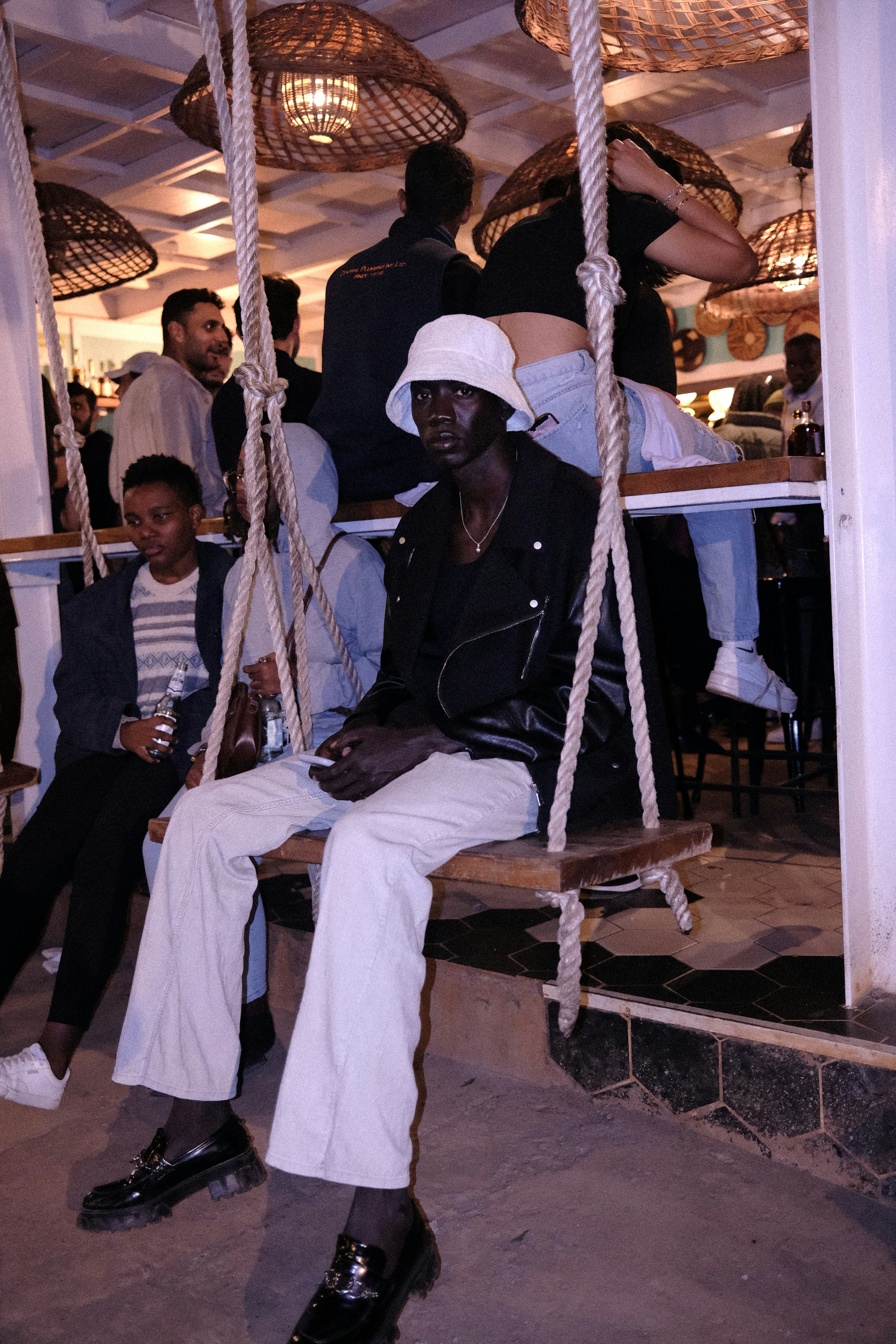 Portrait of Madibo Yut, a fashion designer and model in Nairobi, Kenya | A man sits on a swing at a bar.