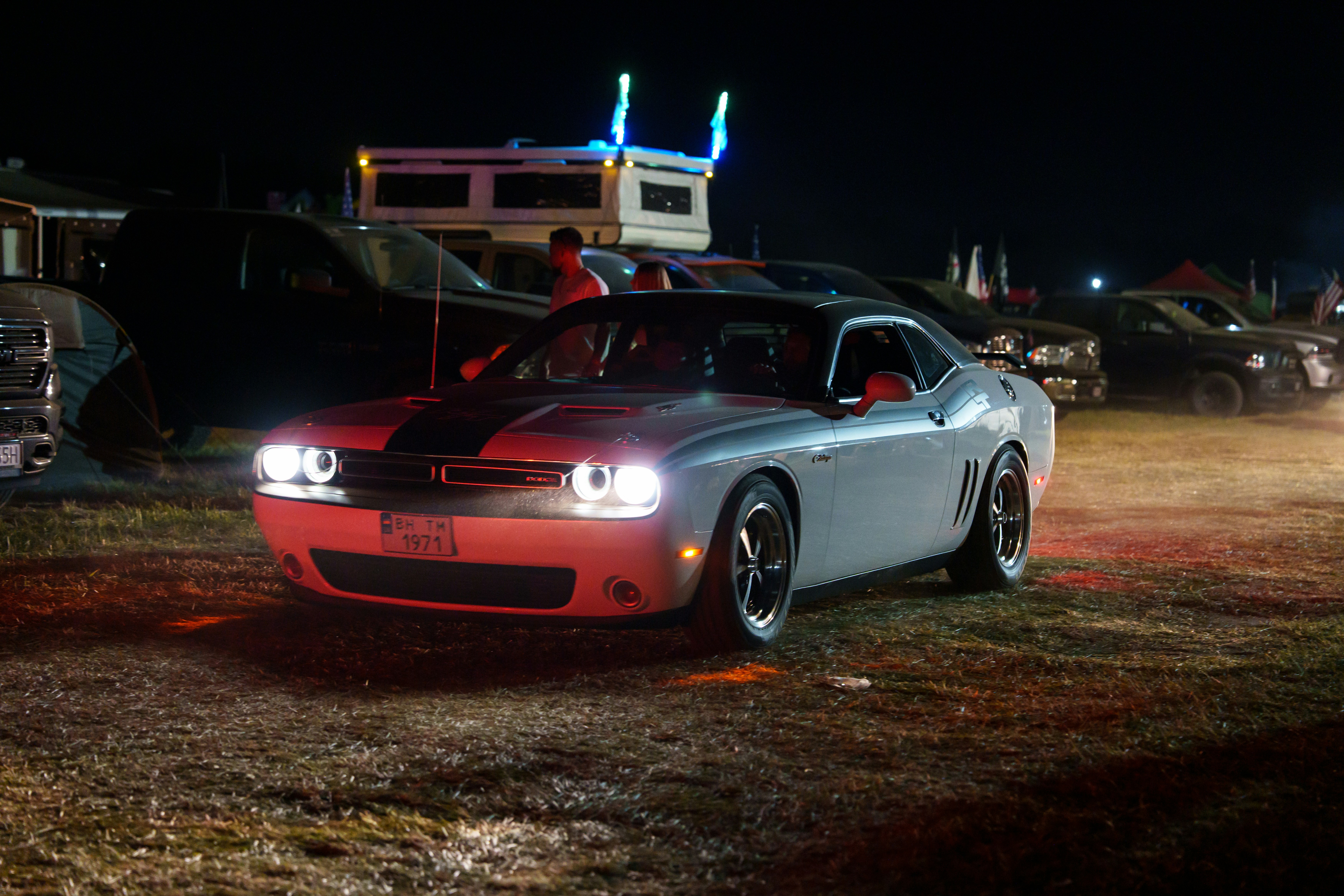 A sleek muscle car illuminated by headlights, parked amidst a lively night scene filled with vehicles and activity.