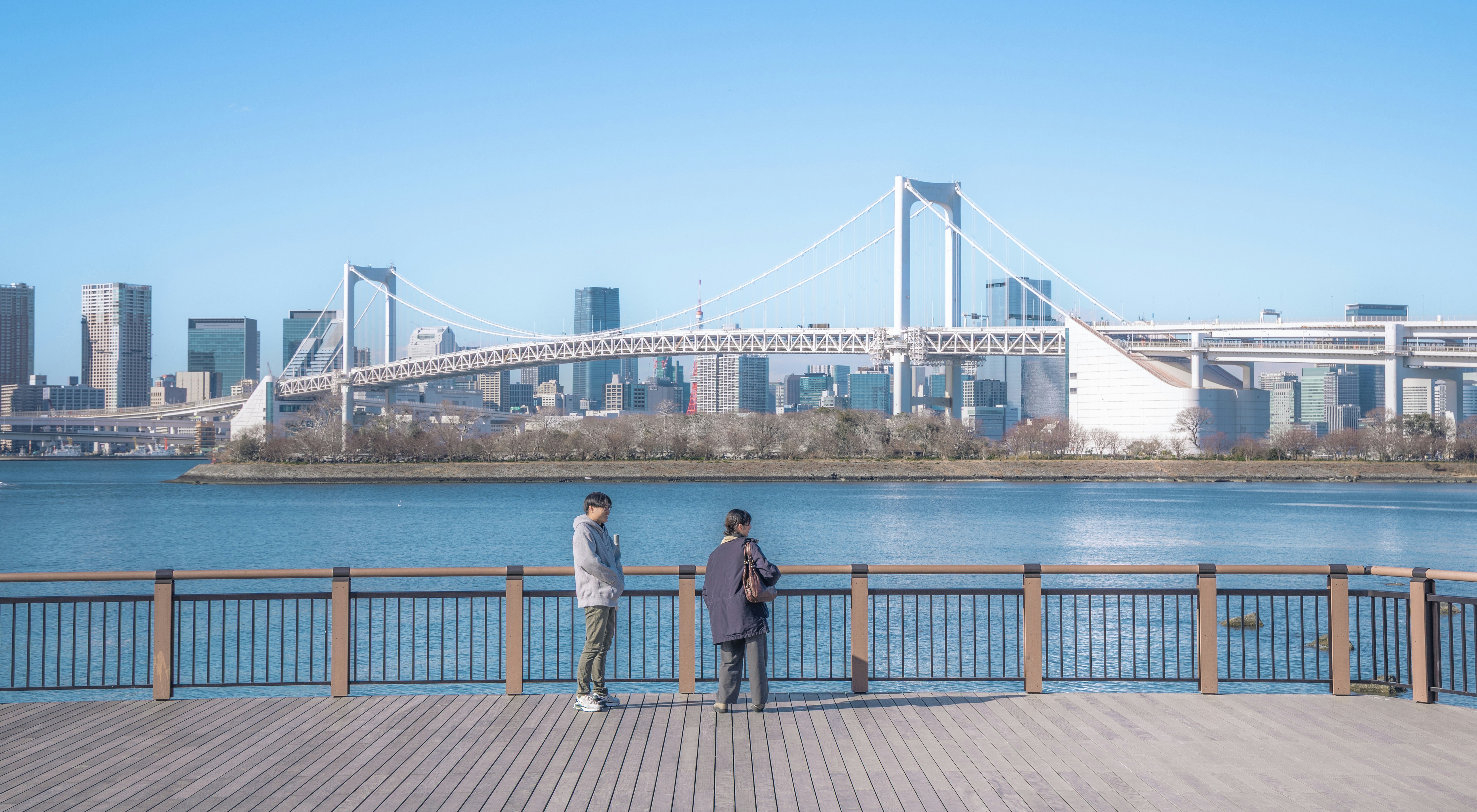 Arc of Steel and Silence: Two Figures at the Waterfront Under a City Bridge