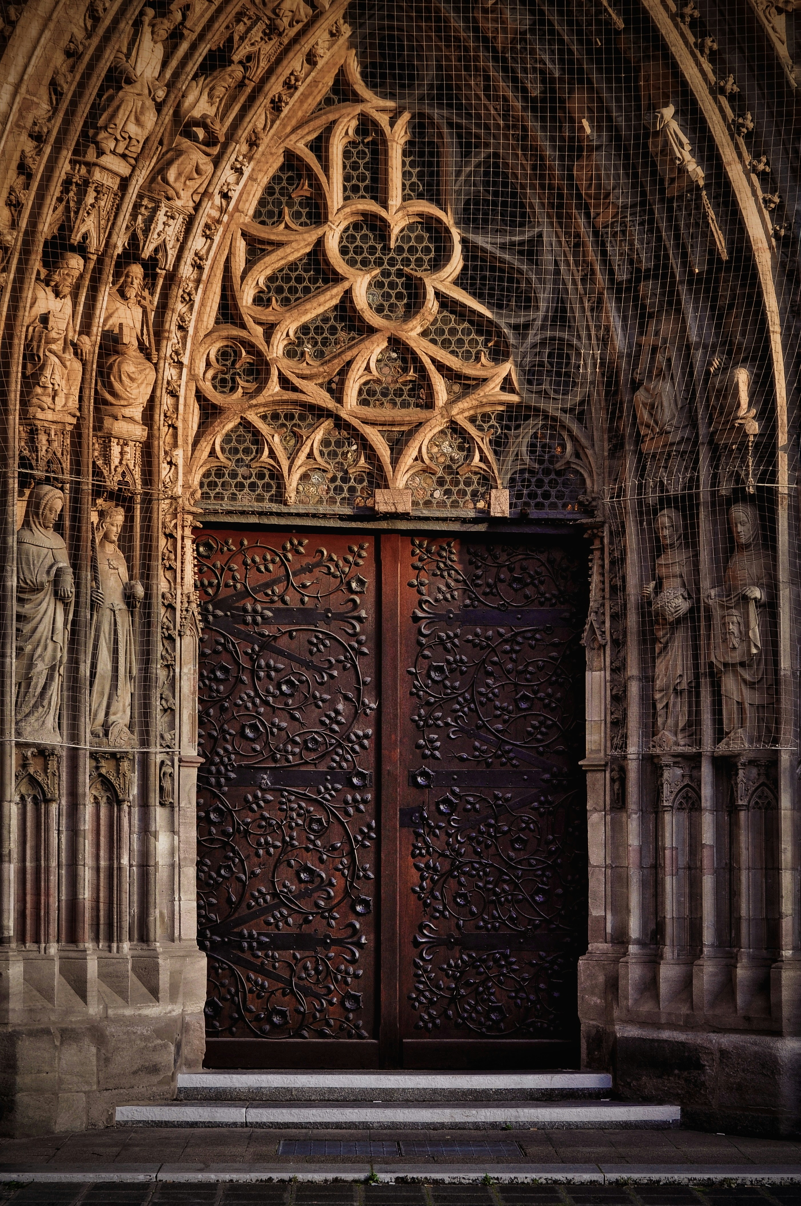 Elaborate wooden doors adorned with intricate carvings, framed by ornate stone arches and statues, showcasing architectural artistry.