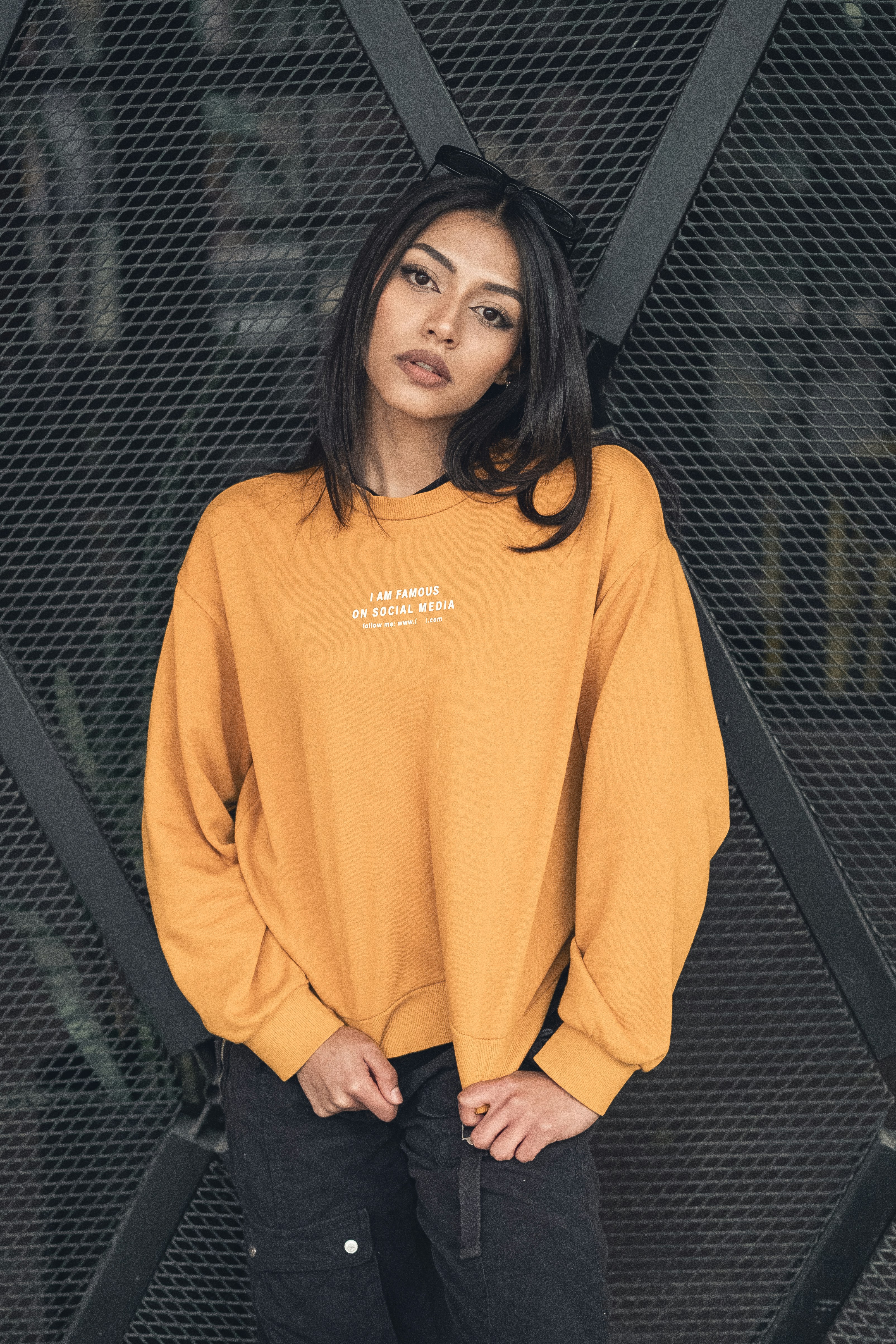 Woman in a sweatshirt poses in front of a metal wall.