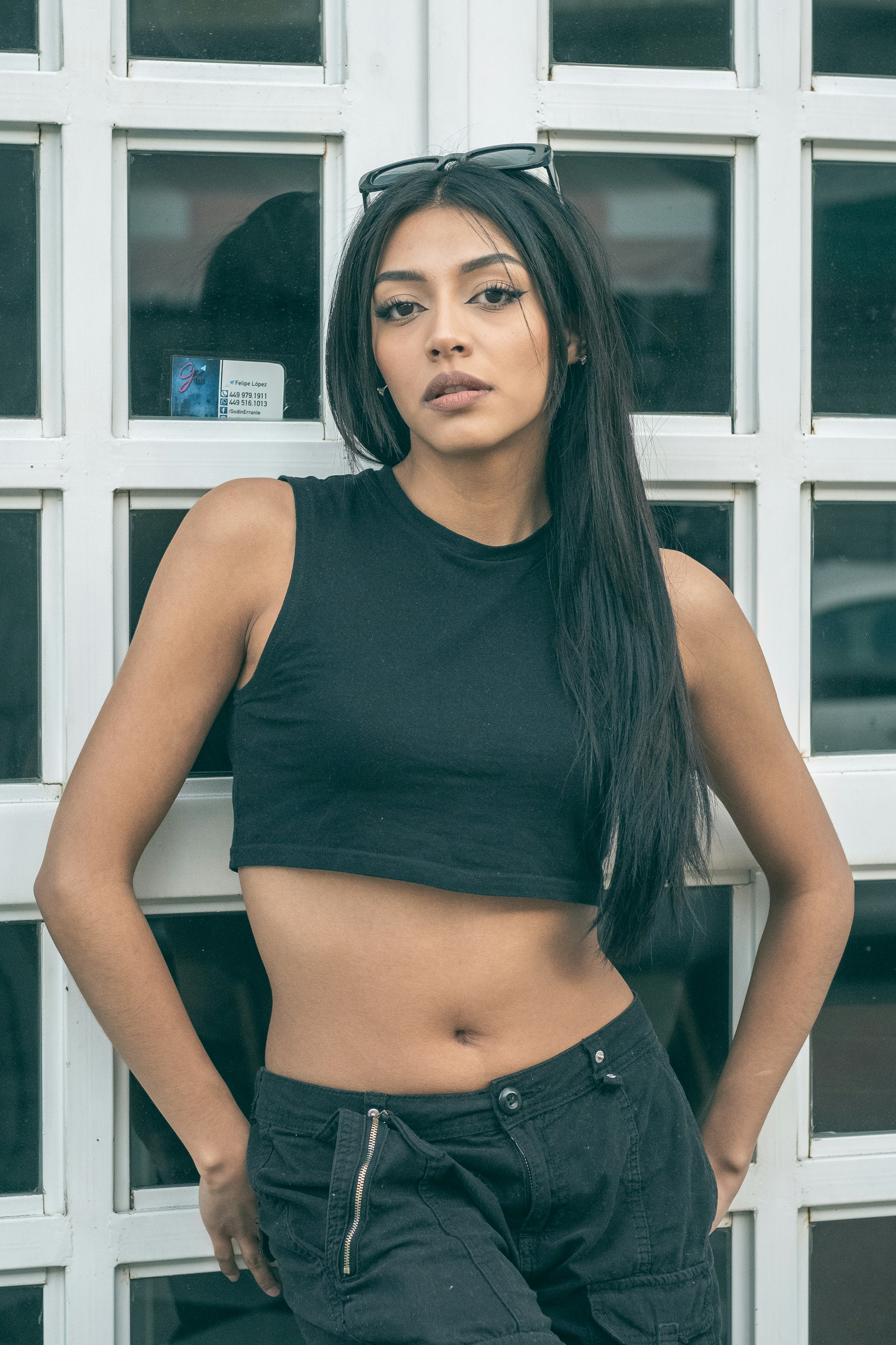 A stylish woman poses confidently in front of windows.