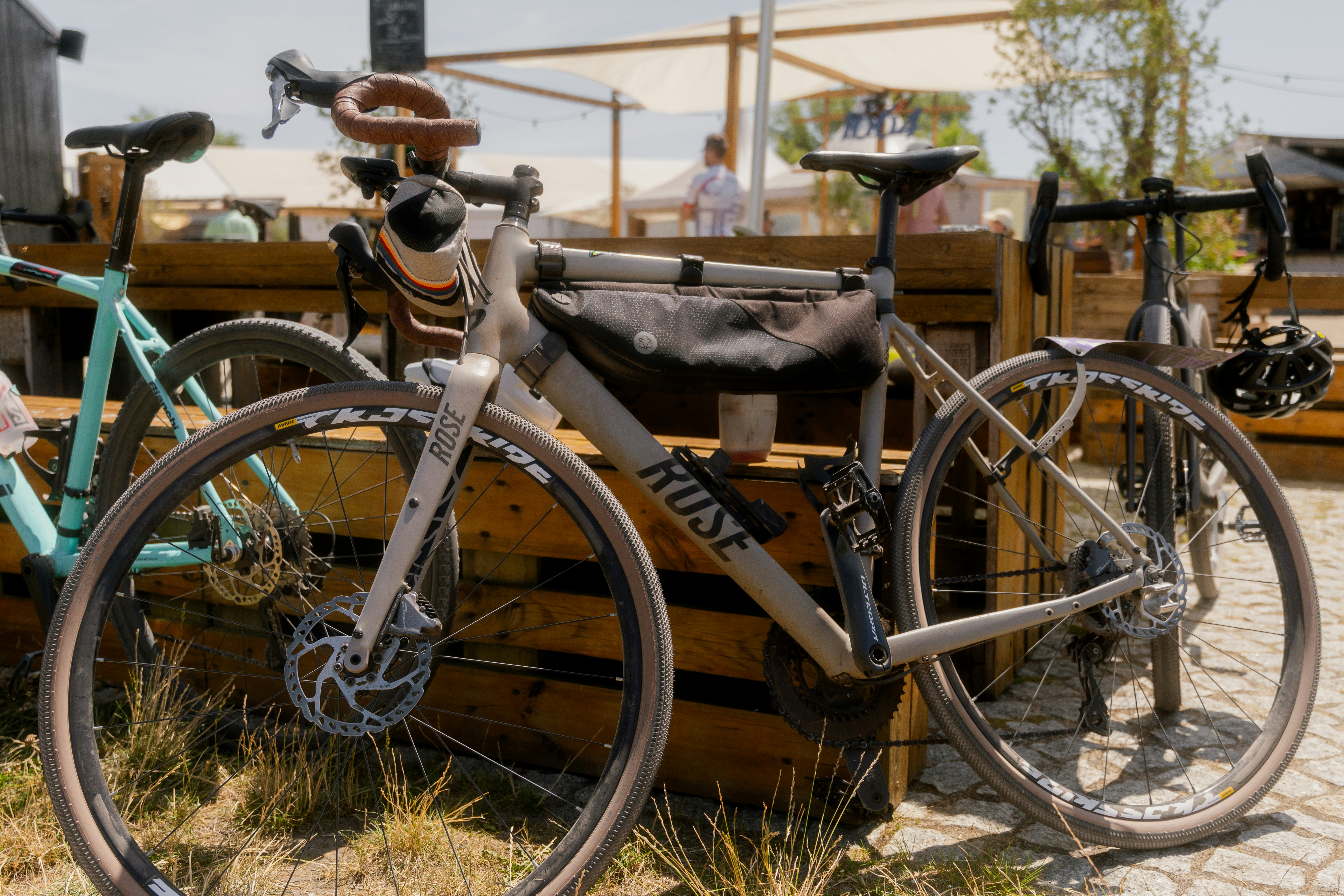 A sleek gravel bike parked beside wooden crates in a lively outdoor setting, showcasing its rugged design and practicality for urban exploration.